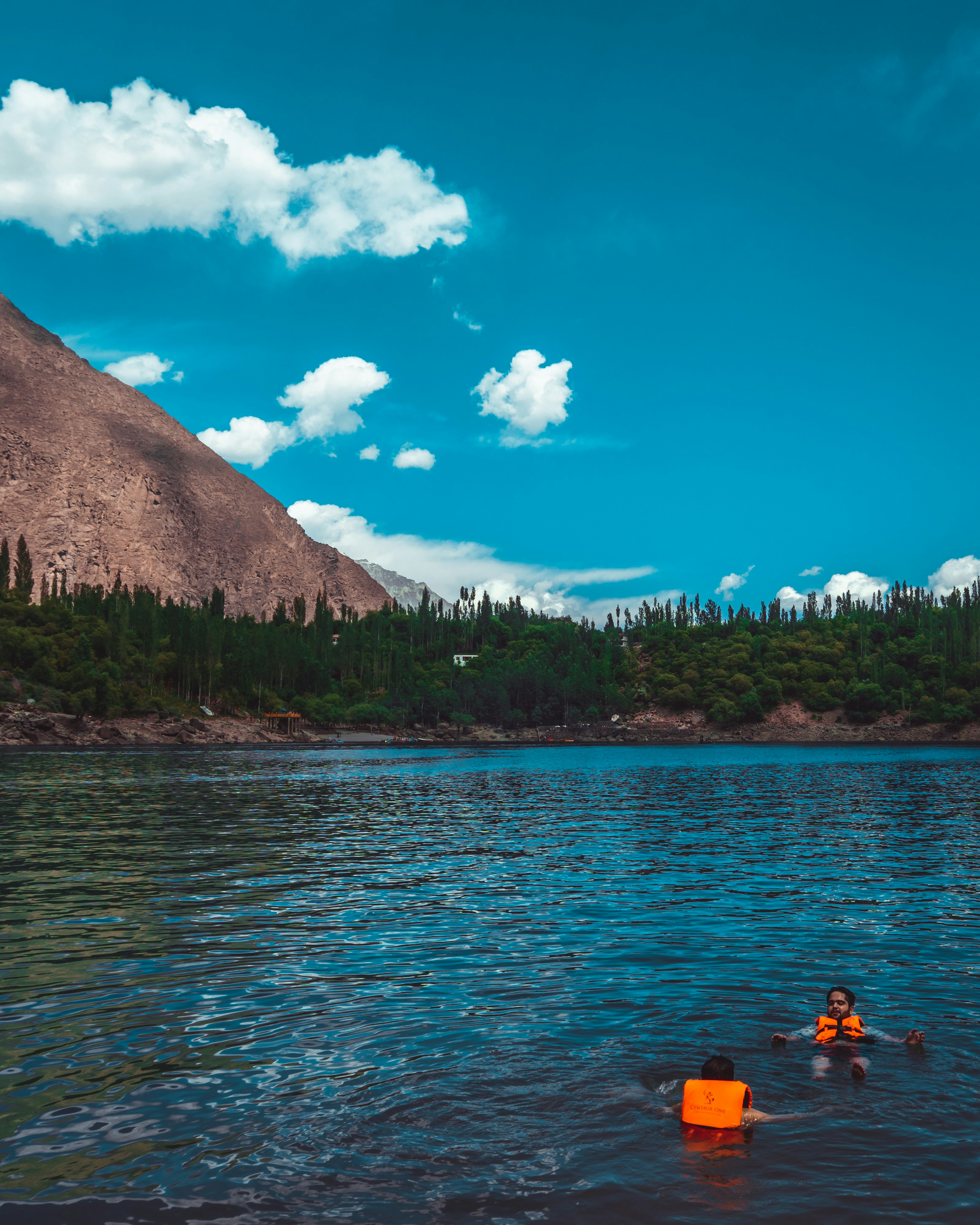 Orange Life Jackets on a Serene Lake Under a Cliff and Forest