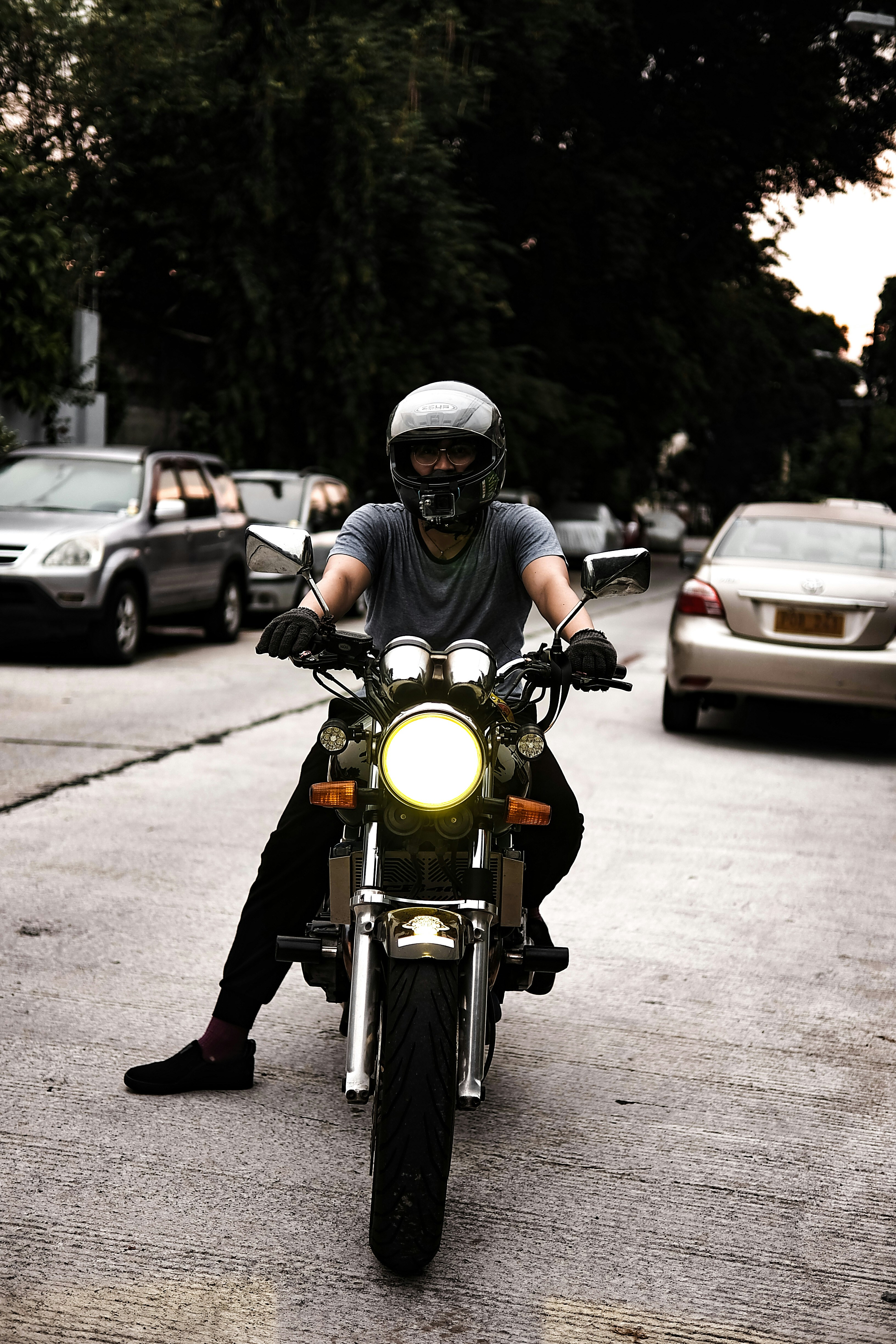Motorcyclist poised on a classic bike in a quiet street, surrounded by parked cars. The scene captures the essence of urban exploration.