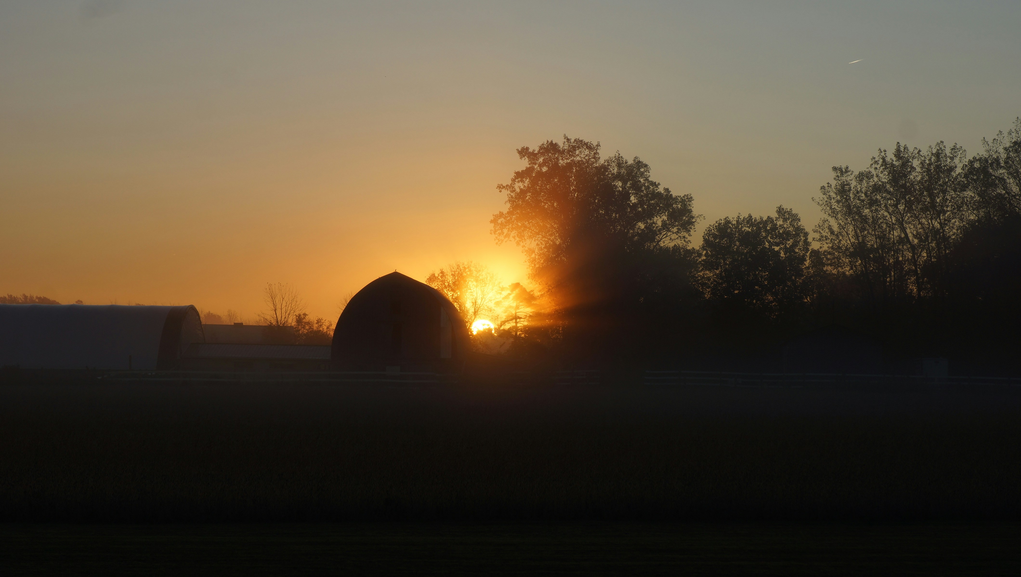 Sunrise through the Quonset: a farm silhouette against a fiery horizon