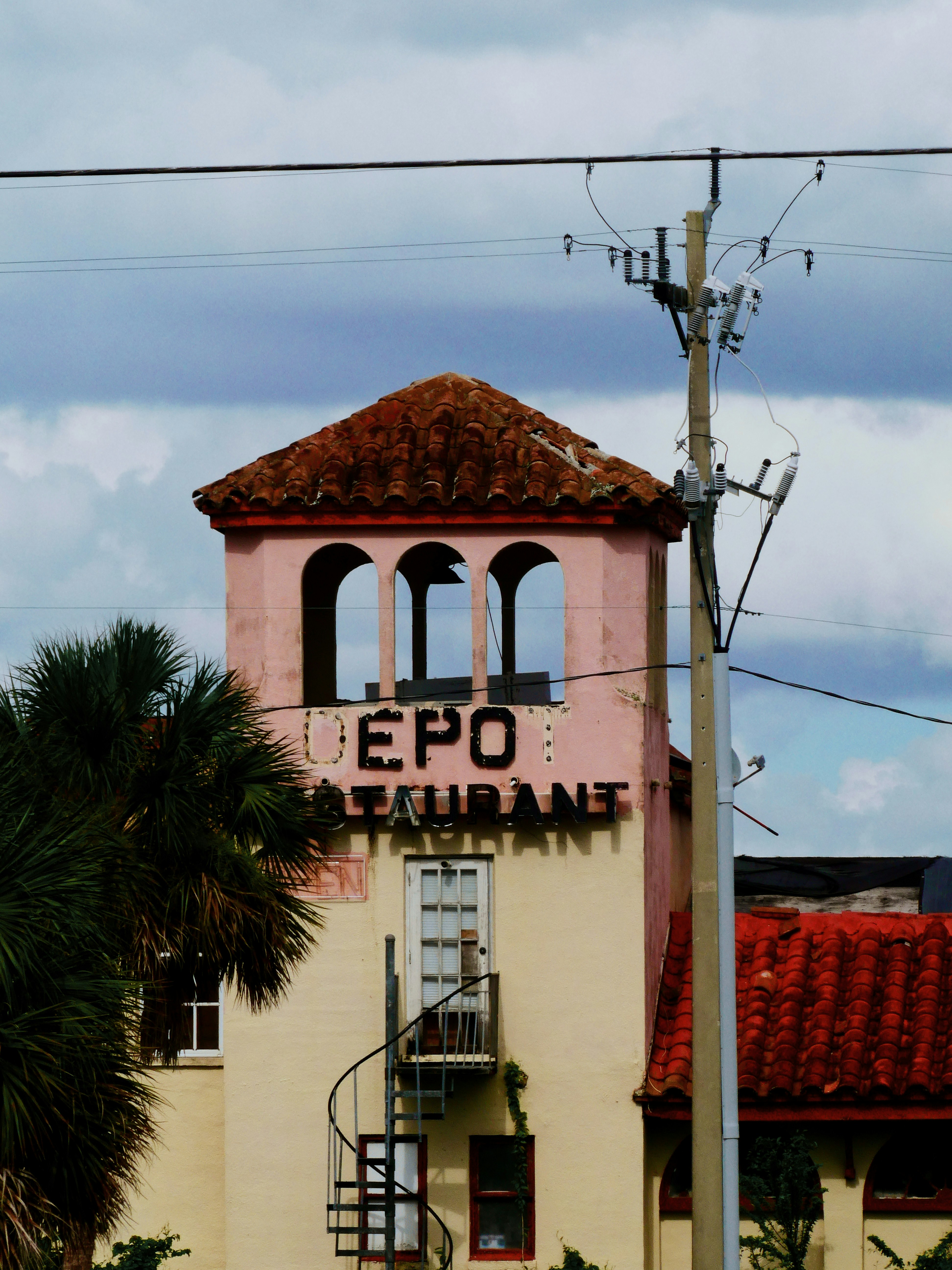 Historic restaurant facade featuring the word 'DEPOT' prominently displayed, surrounded by lush greenery and power lines. A blend of architectural styles is evident.