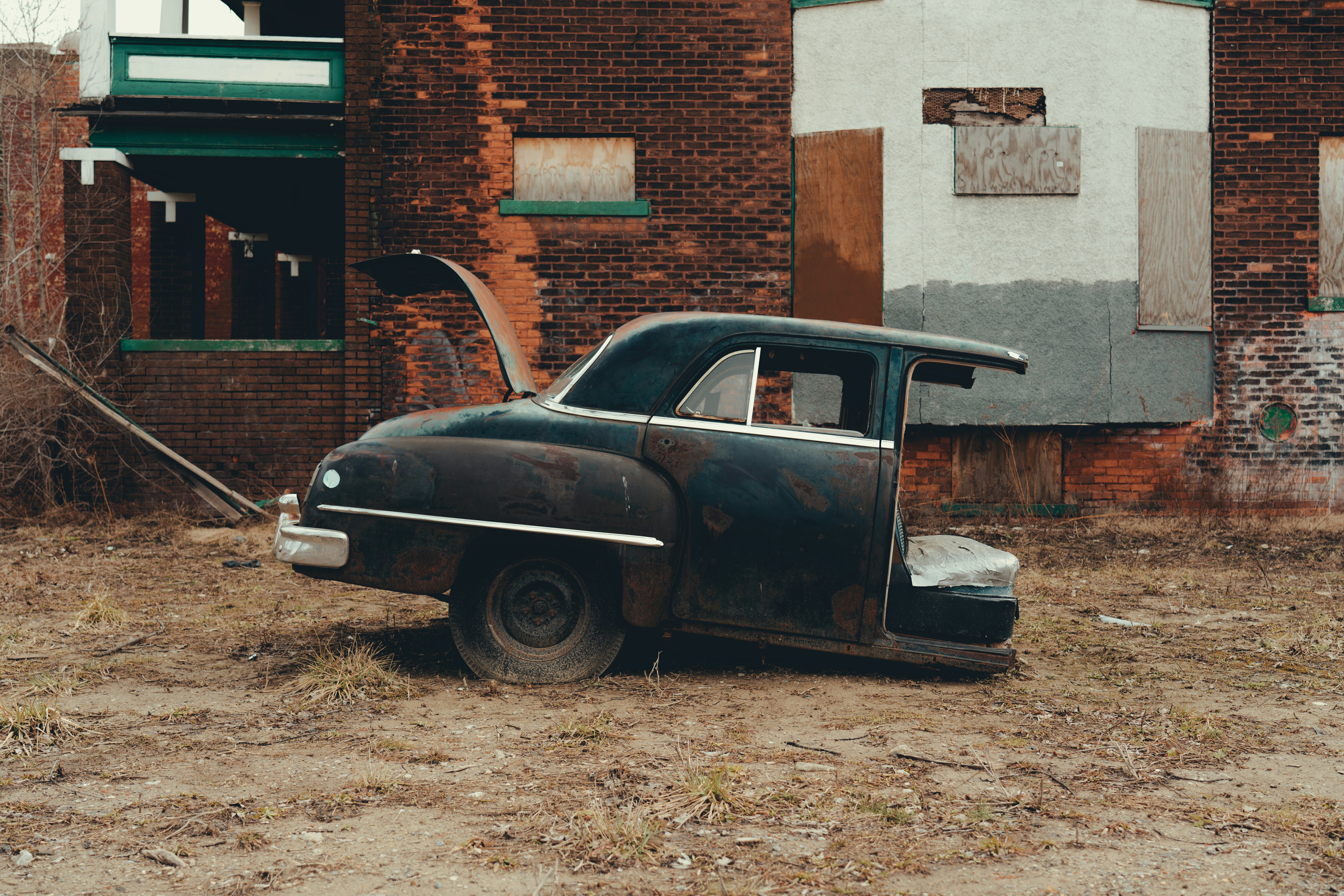 Abandoned vintage car resting in a desolate lot beside a dilapidated building, showcasing signs of age and neglect.