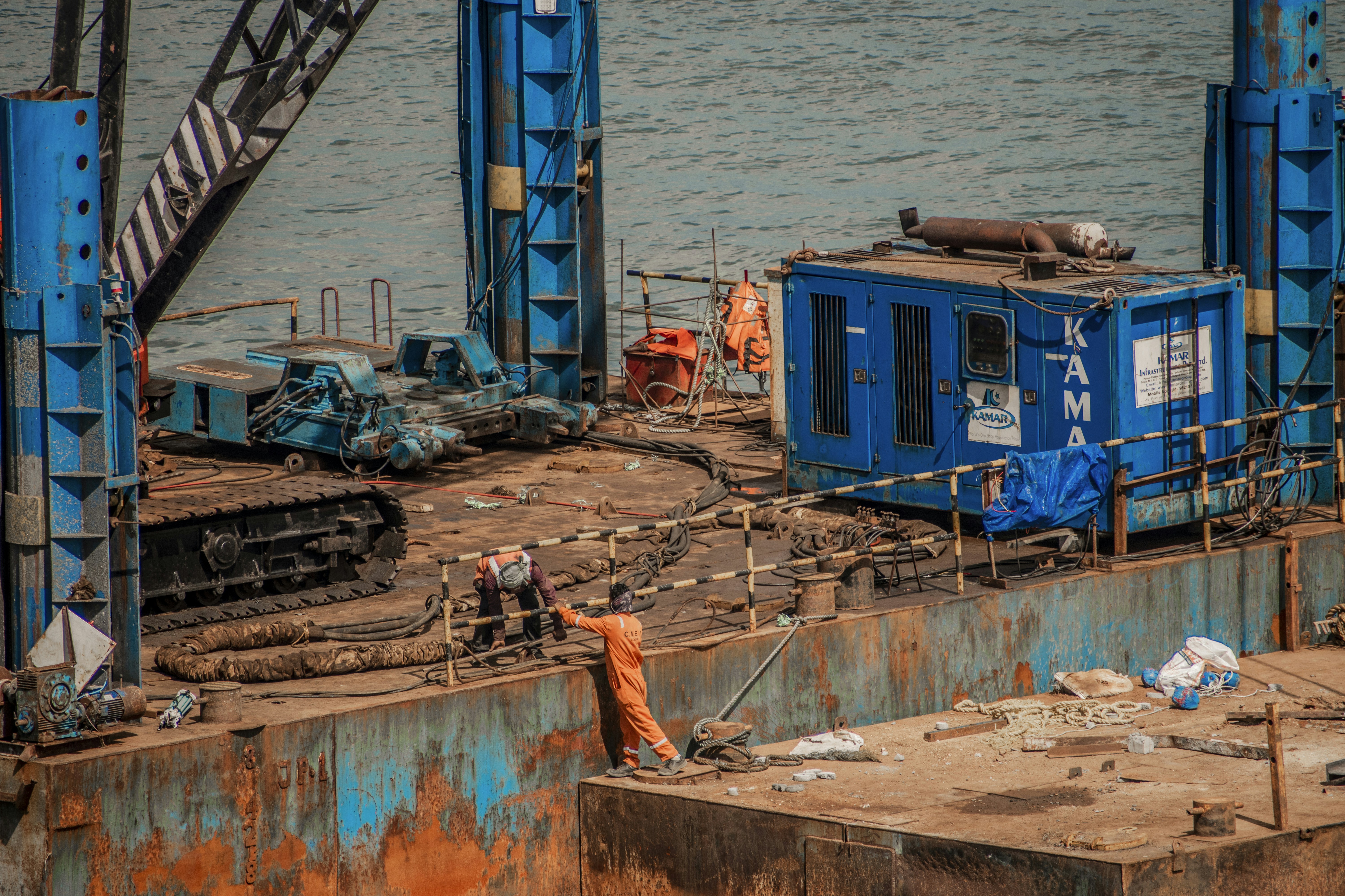 Orange Clad Worker at a Rusted Dock Under Blue Machinery