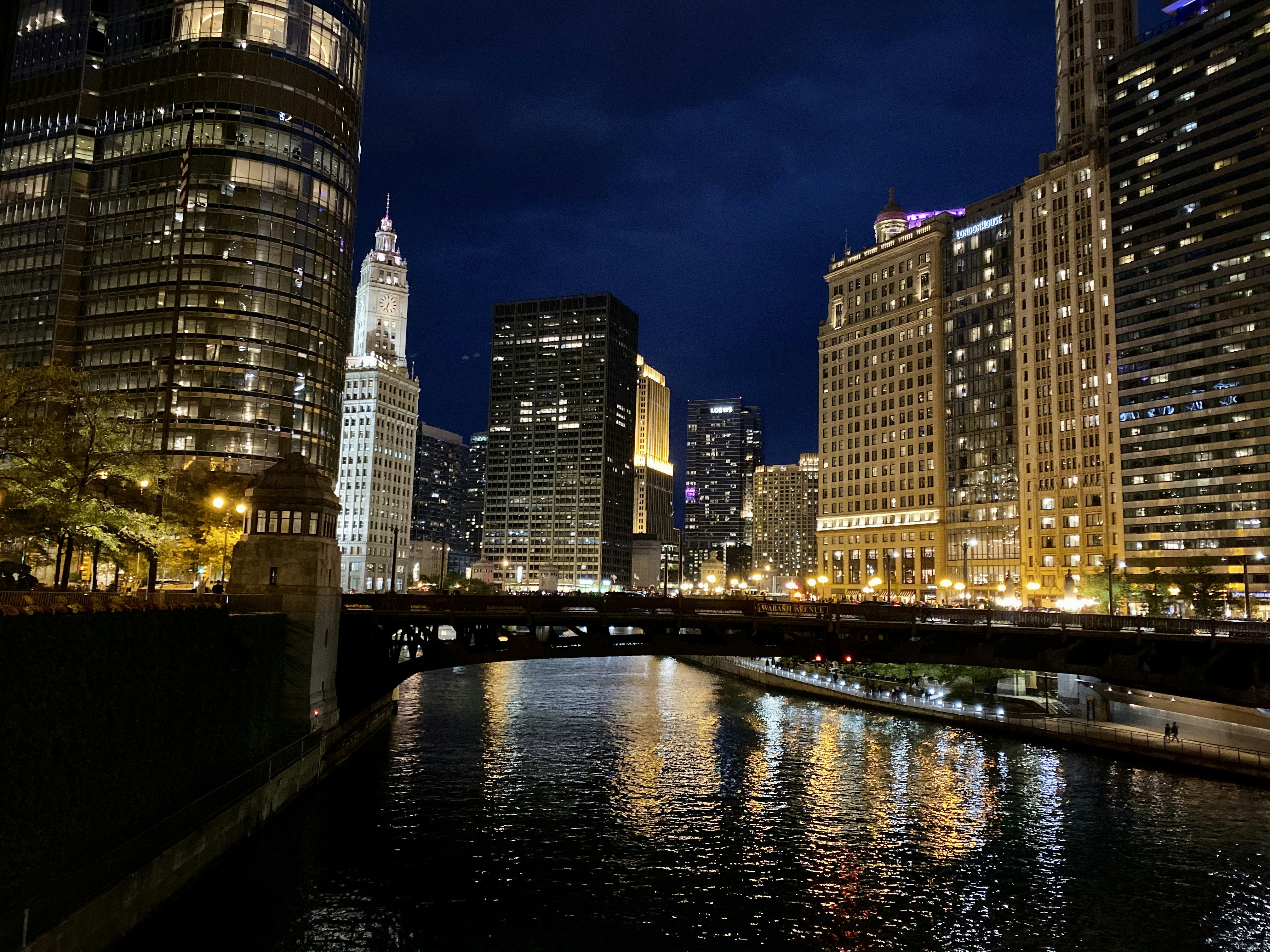 Illuminated skyline reflecting on the calm waters of a city river at night, showcasing architectural highlights and vibrant city life.