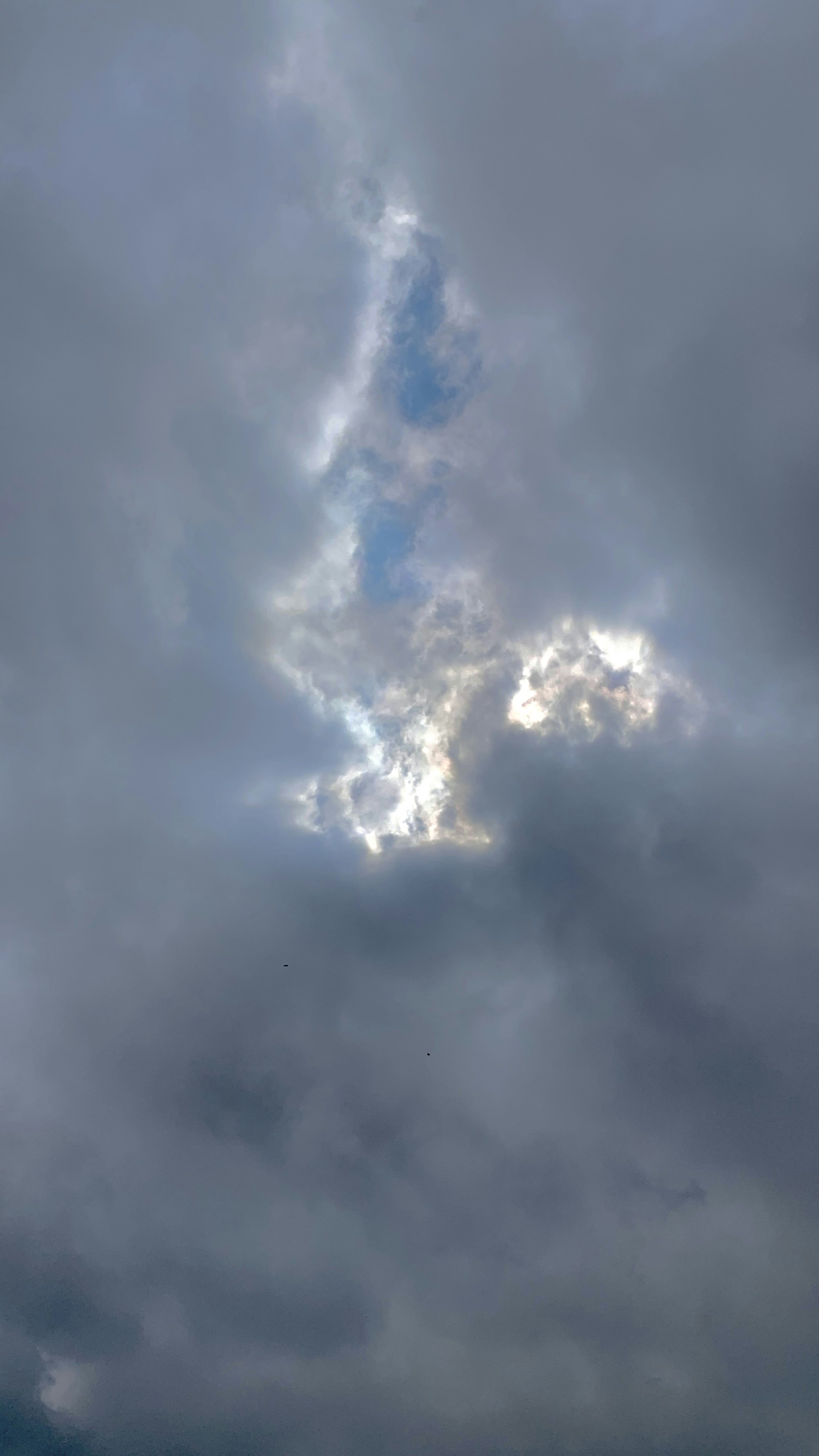 Dramatic cloud cover with a narrow opening revealing a patch of blue sky and soft light. The scene conveys a sense of mystery and tranquility.