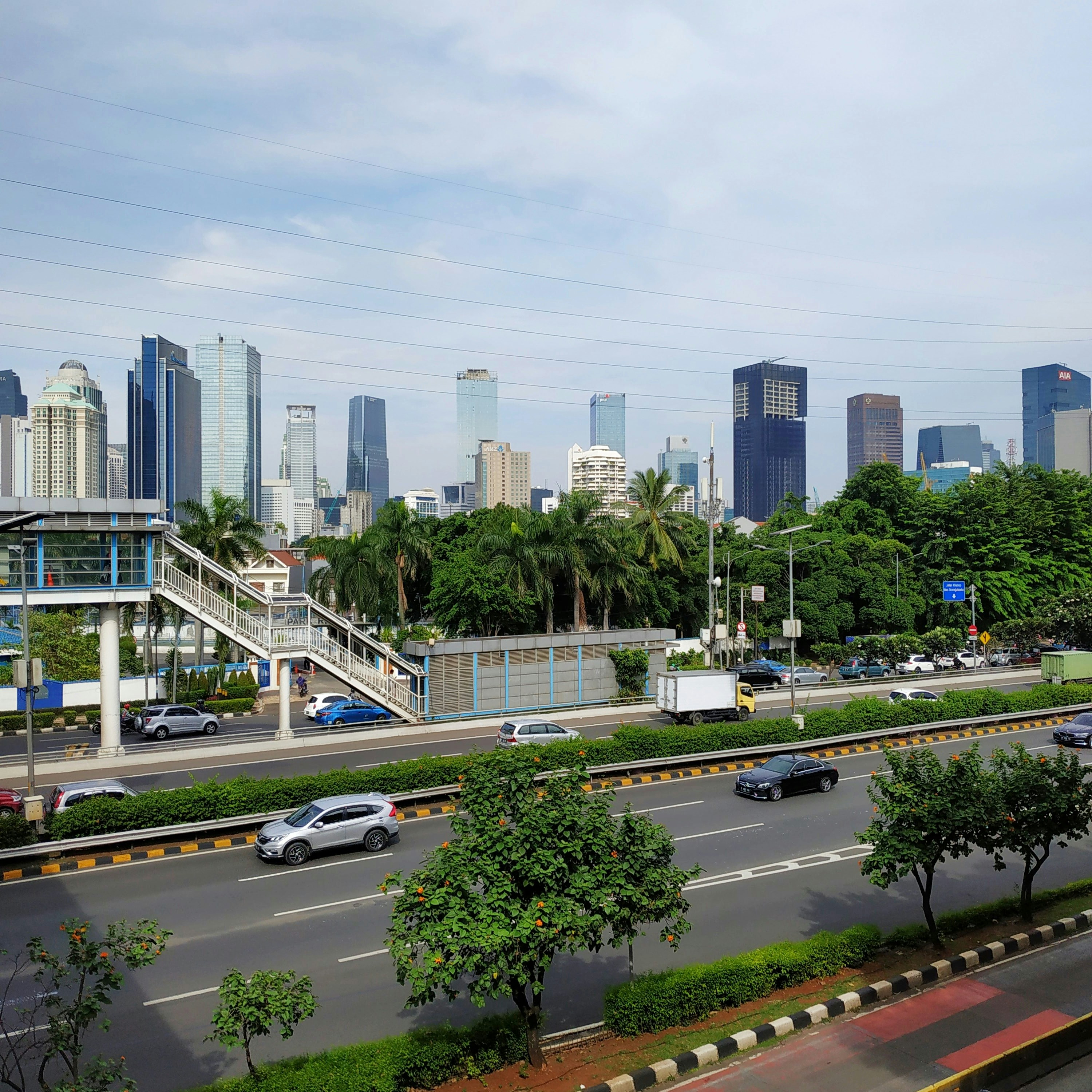 A bustling cityscape featuring modern skyscrapers, lush greenery, and busy roads, showcasing urban life in motion.