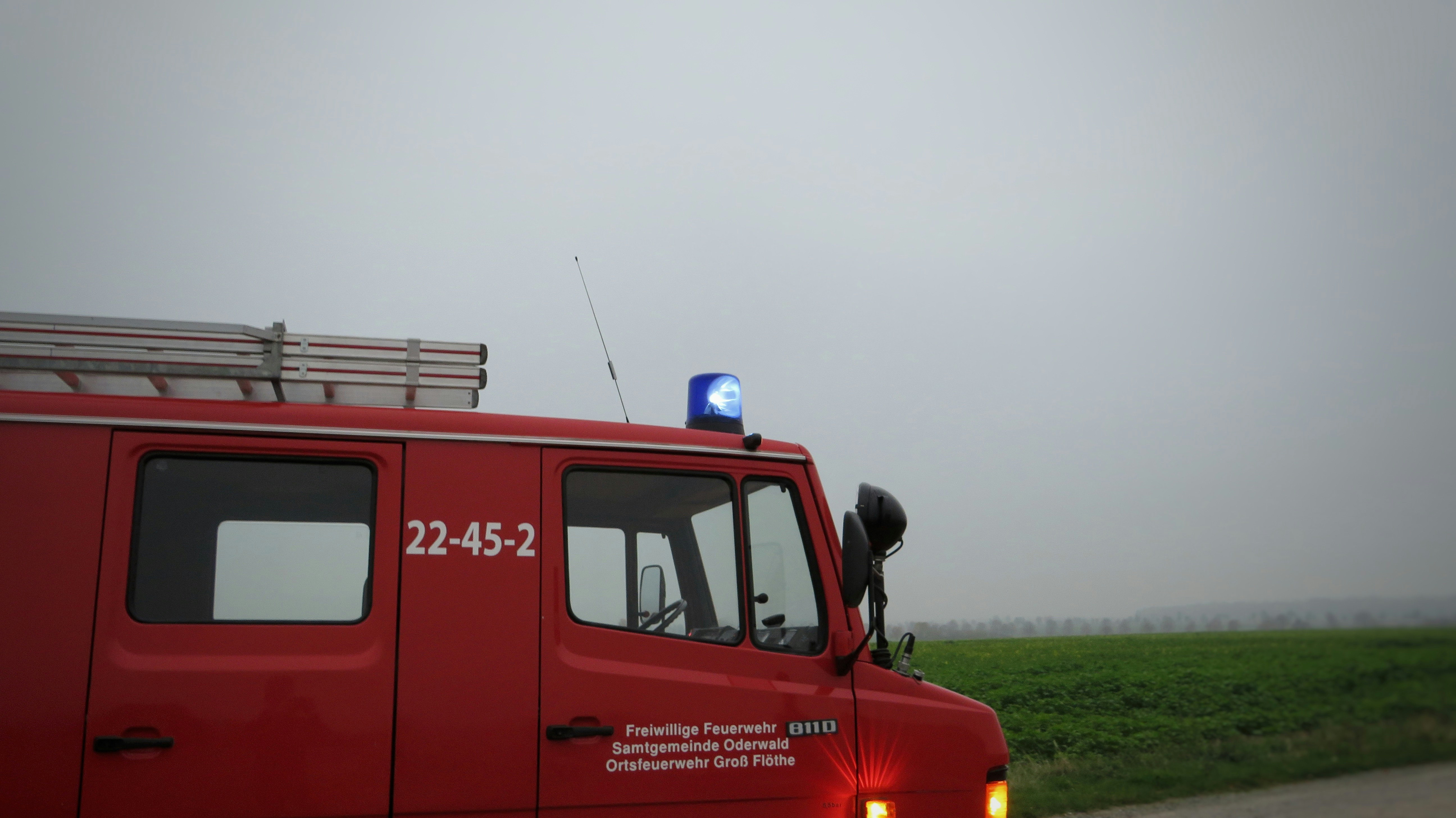 Red firetruck with blue light on a foggy roadside field.