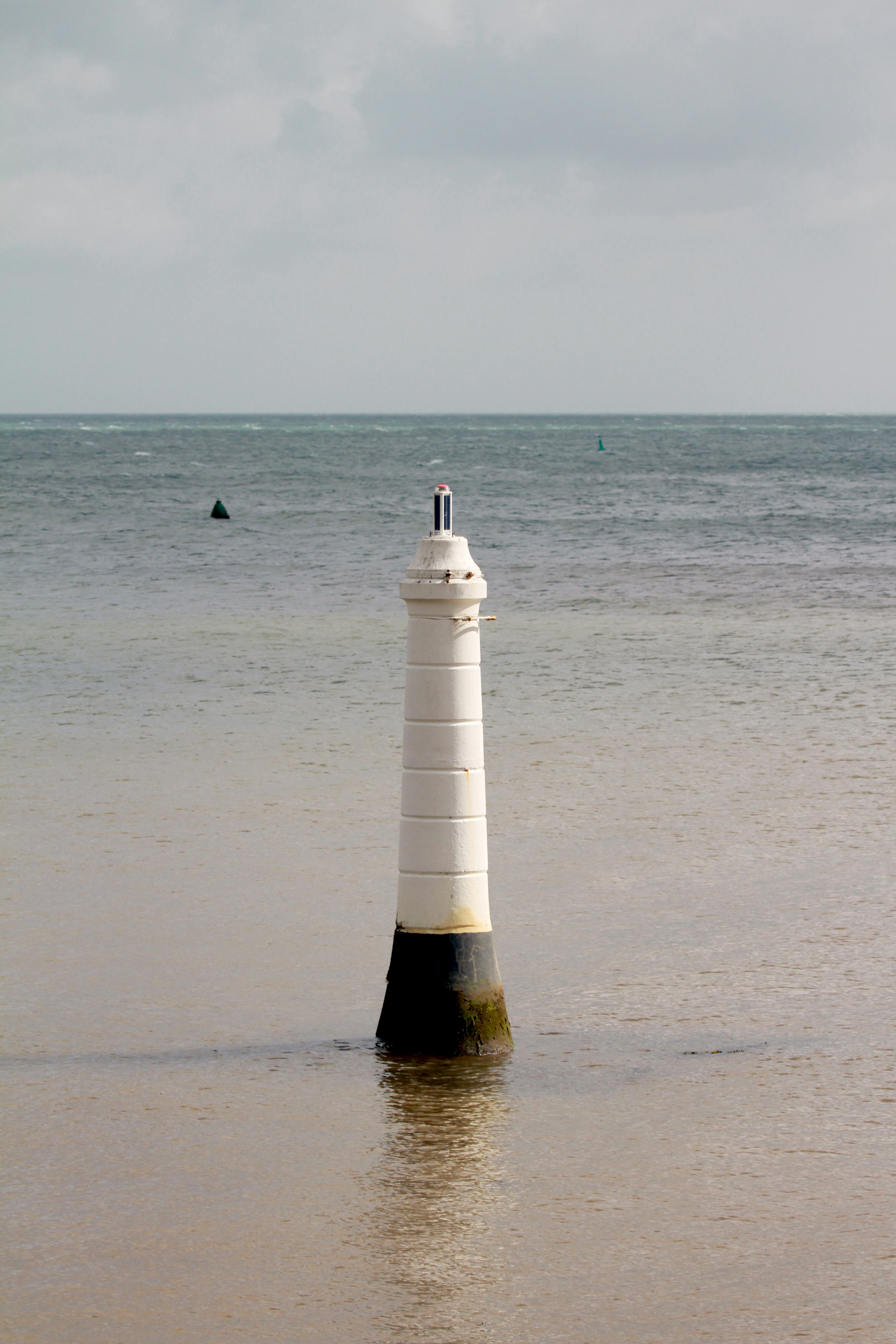 Beacon at the Edge: A White Lighthouse Emerges from Calm Tidal Waters