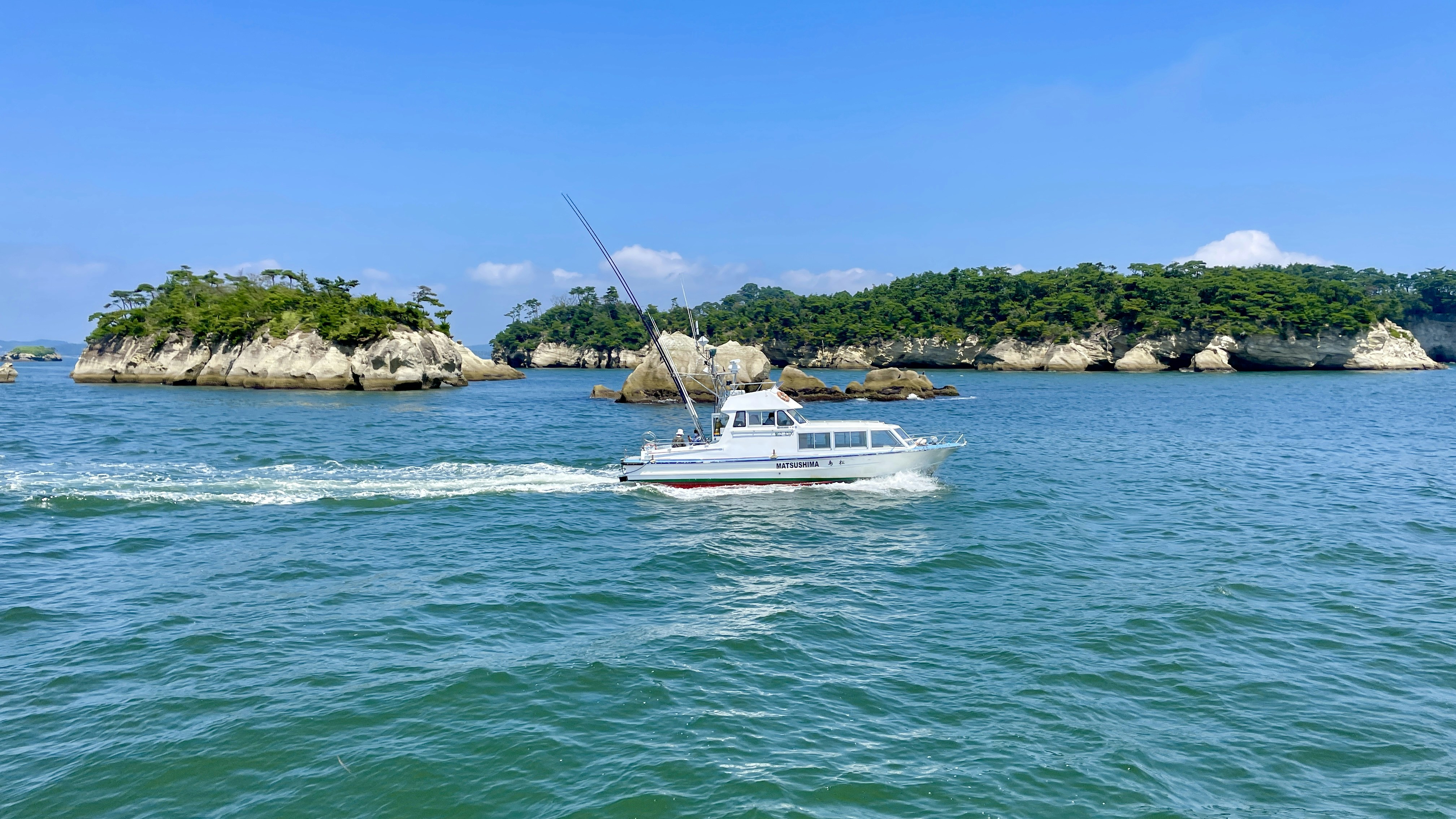White-cabin motorboat gliding through turquoise bay past tree-covered islets