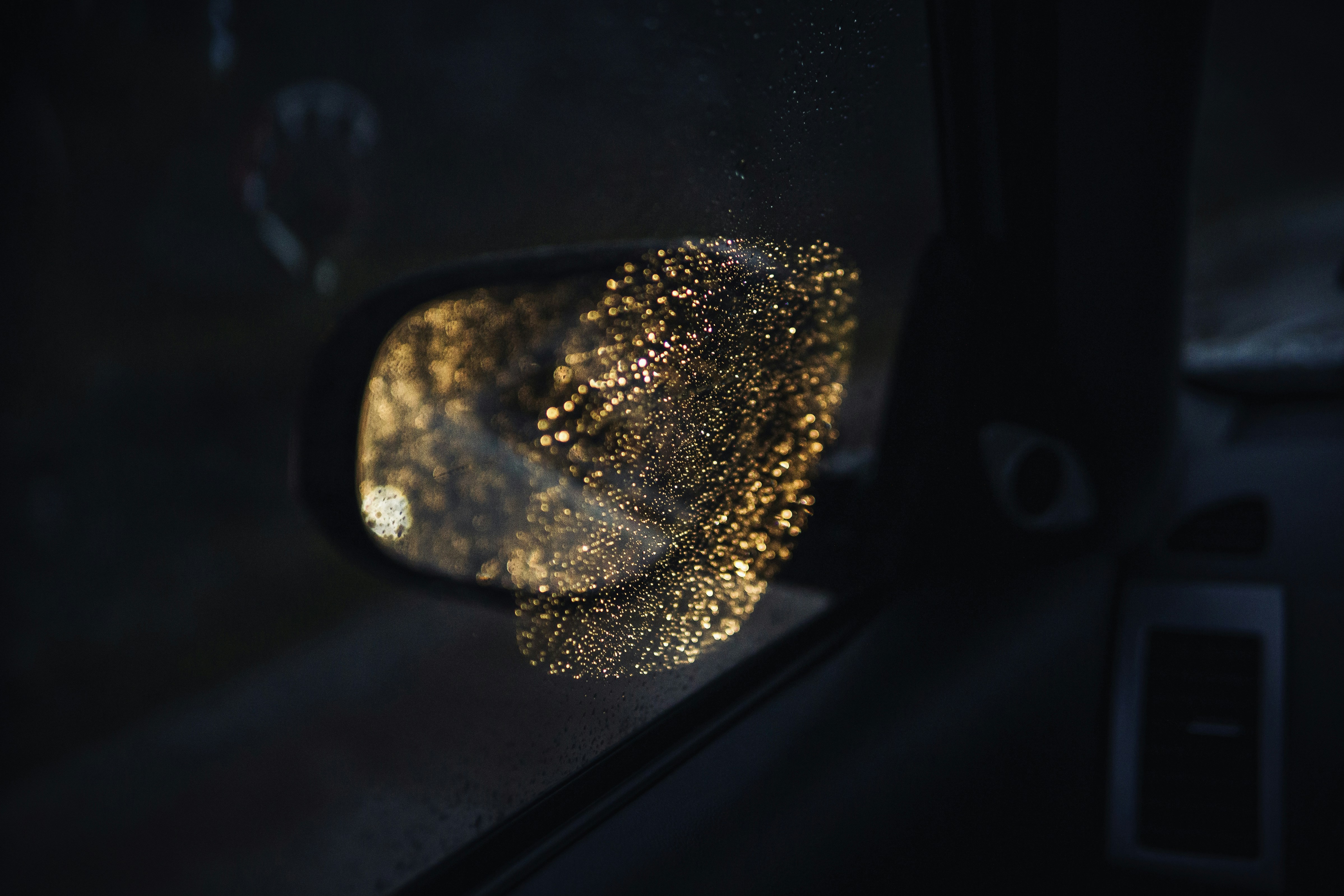 Amber Orbs on a Rain-Kissed Side Mirror at Night