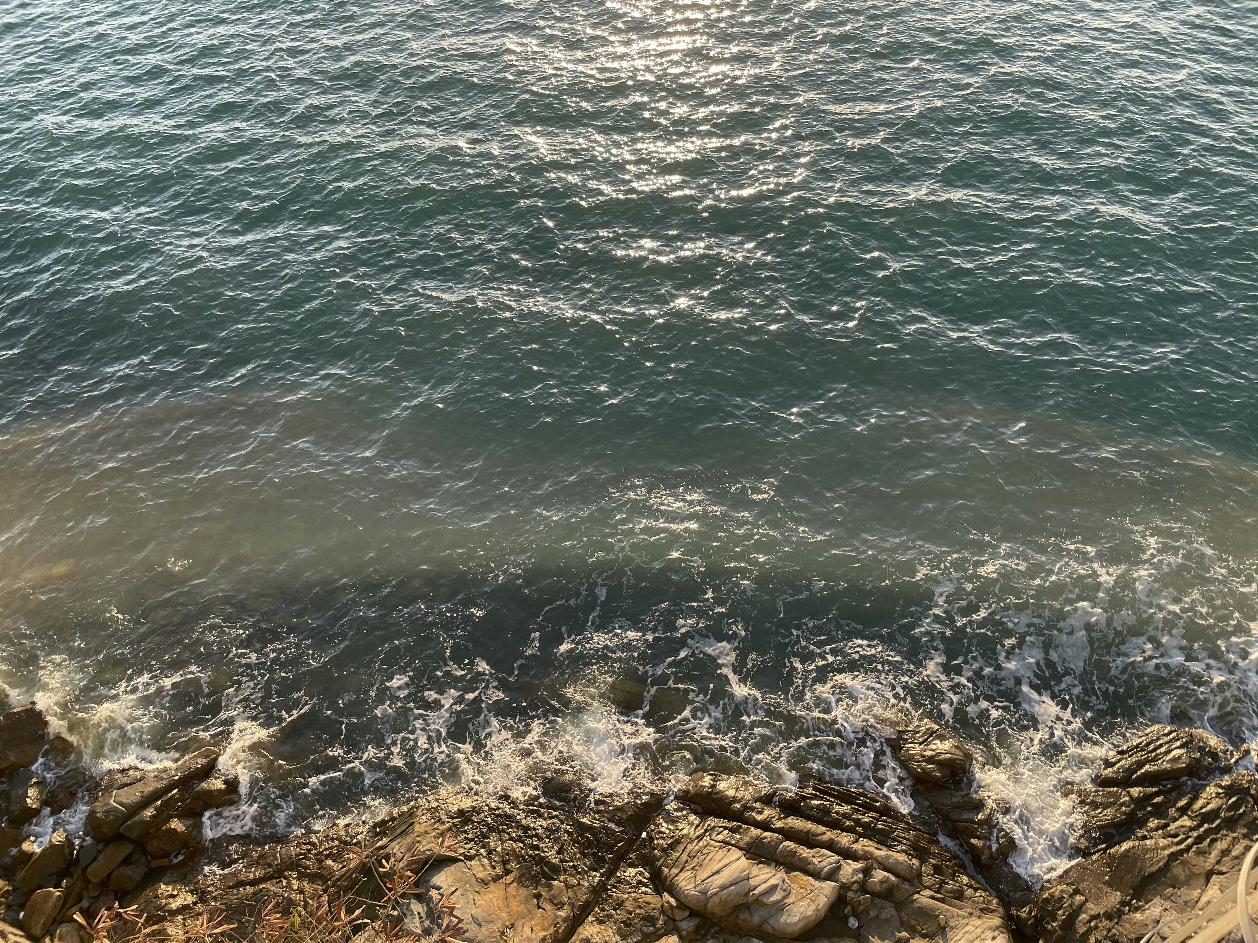 green water waves hitting brown rocks during daytime