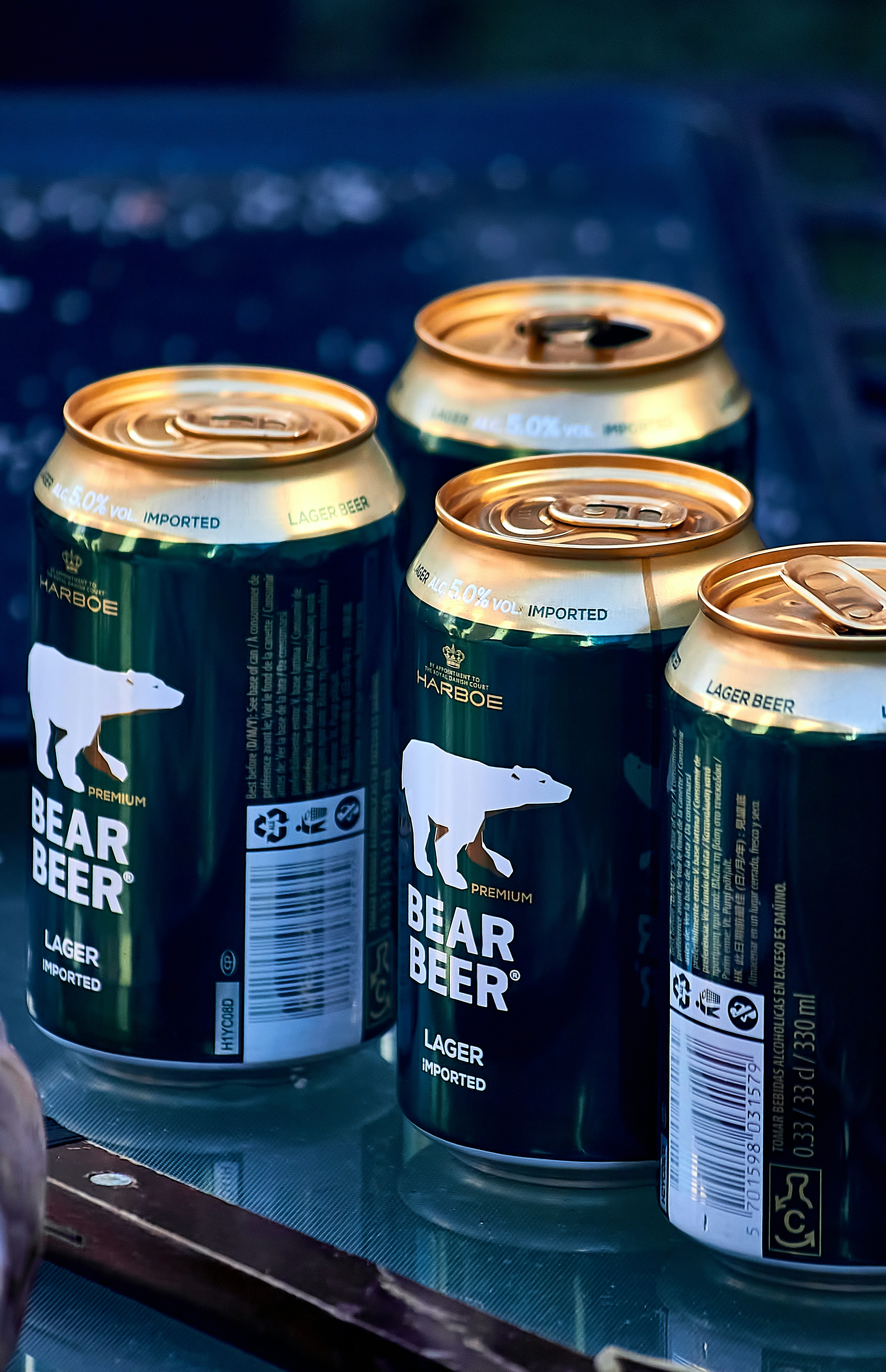 Four cans of Bear Beer arranged on a reflective surface, showcasing their vibrant green design and golden tops.