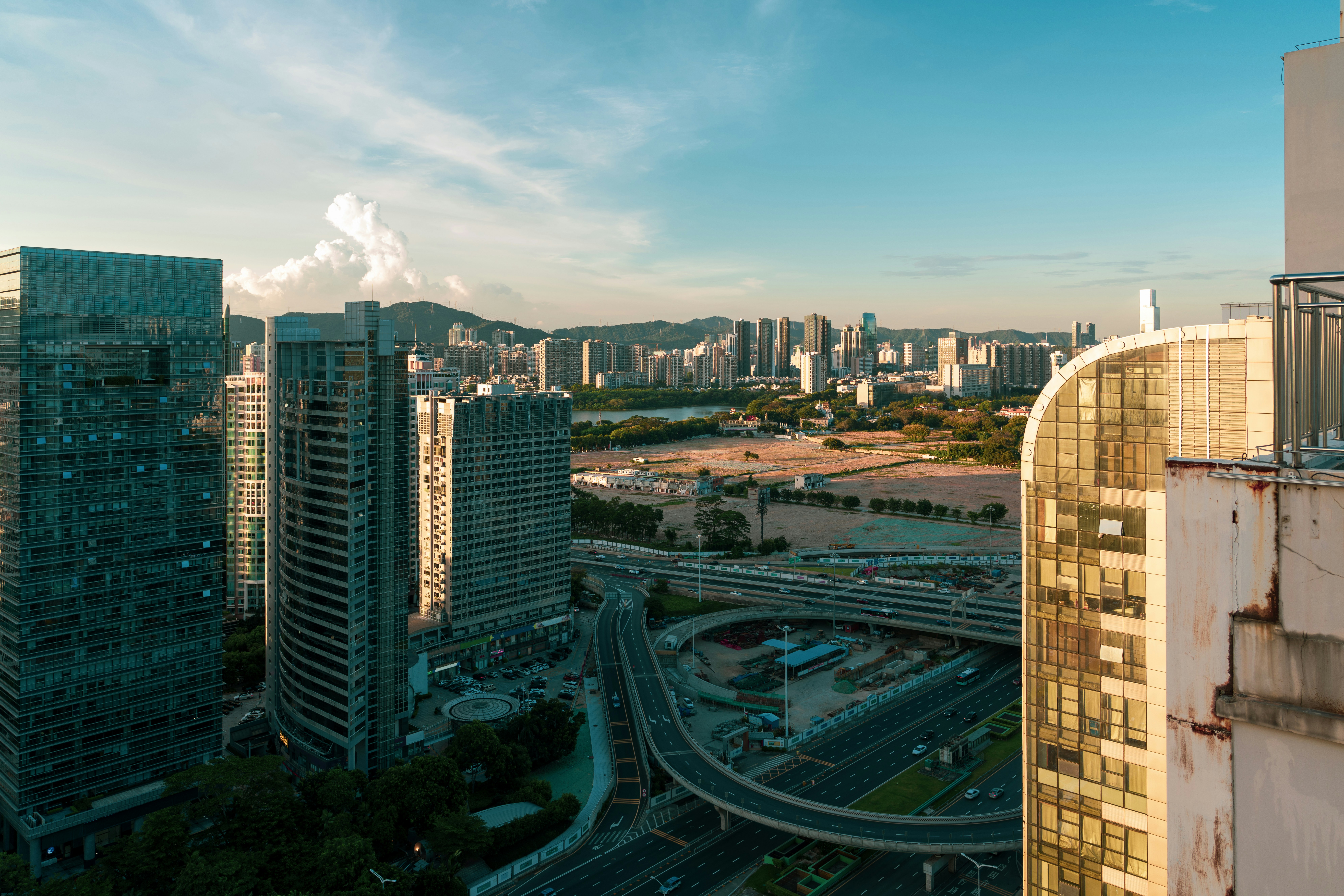 A panoramic view of a bustling urban landscape showcasing skyscrapers and a winding highway under a clear sky. The scene captures the dynamic essence of city life.