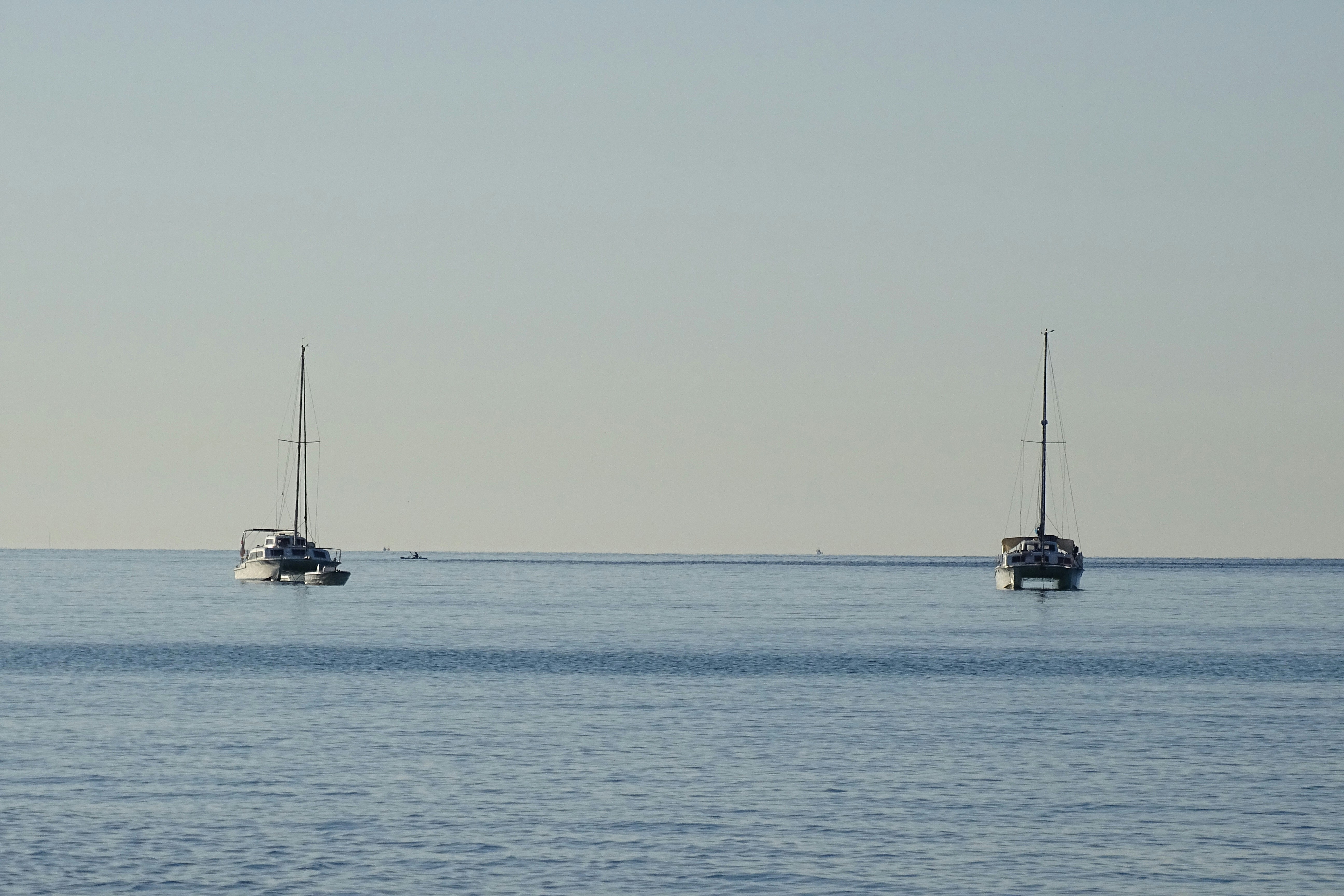 Two sailboats gently floating on calm waters under a clear sky, evoking a sense of tranquility and adventure.