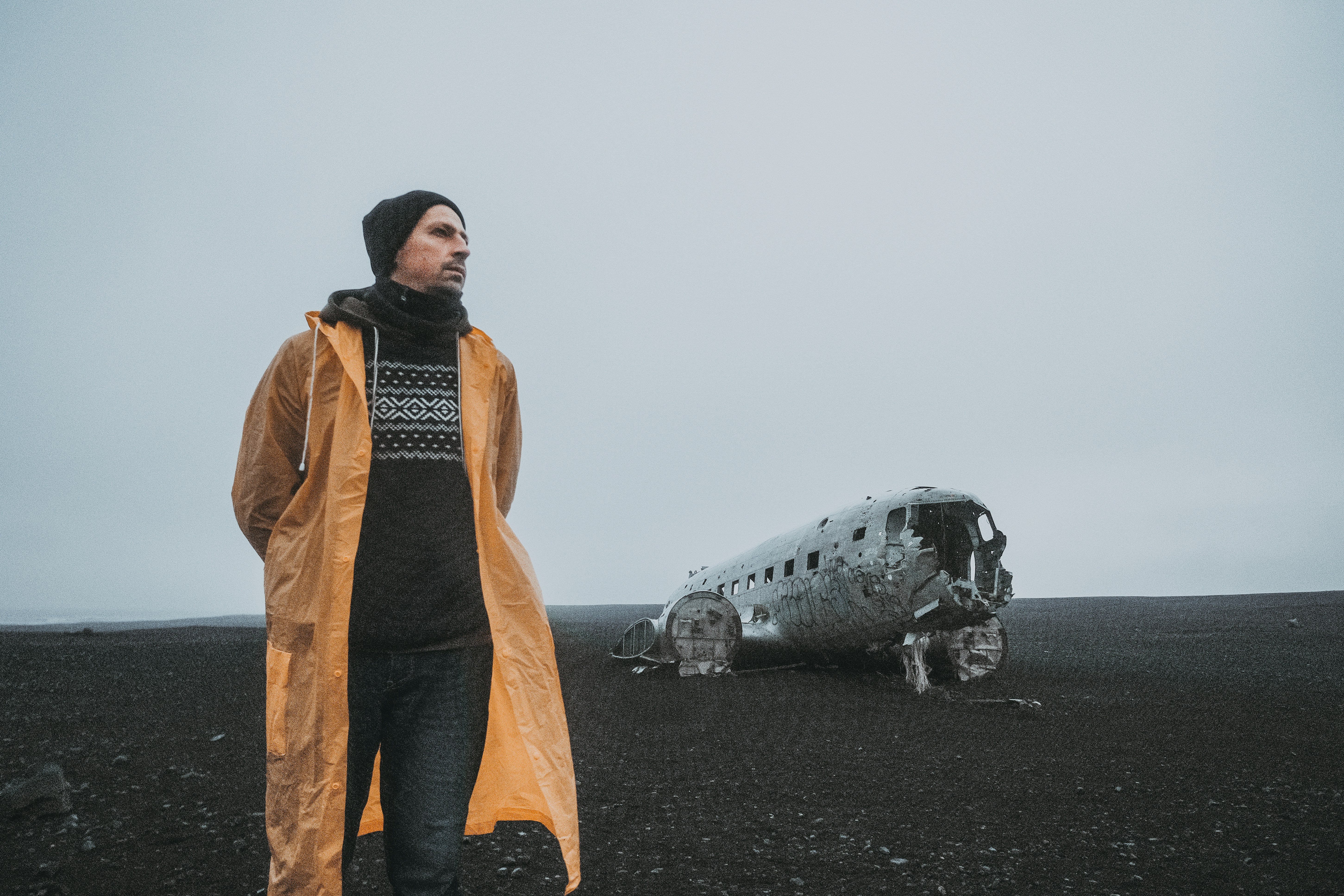 Orange Coat Against a Void: A Traveler Beside a Rusted Wreck on a Volcanic Plain