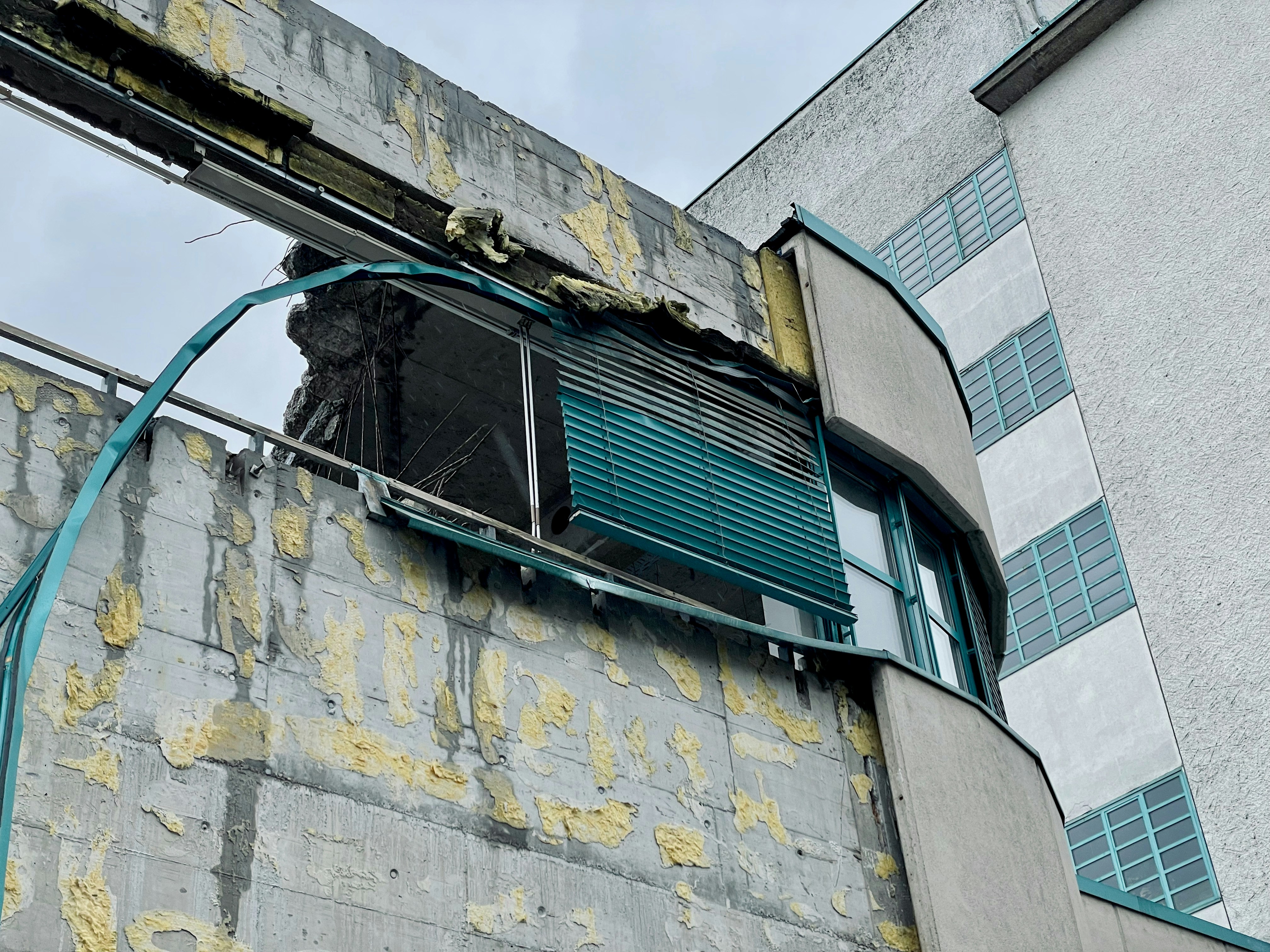 Damaged building facade revealing exposed structures and a broken window, showcasing urban decay and neglect.