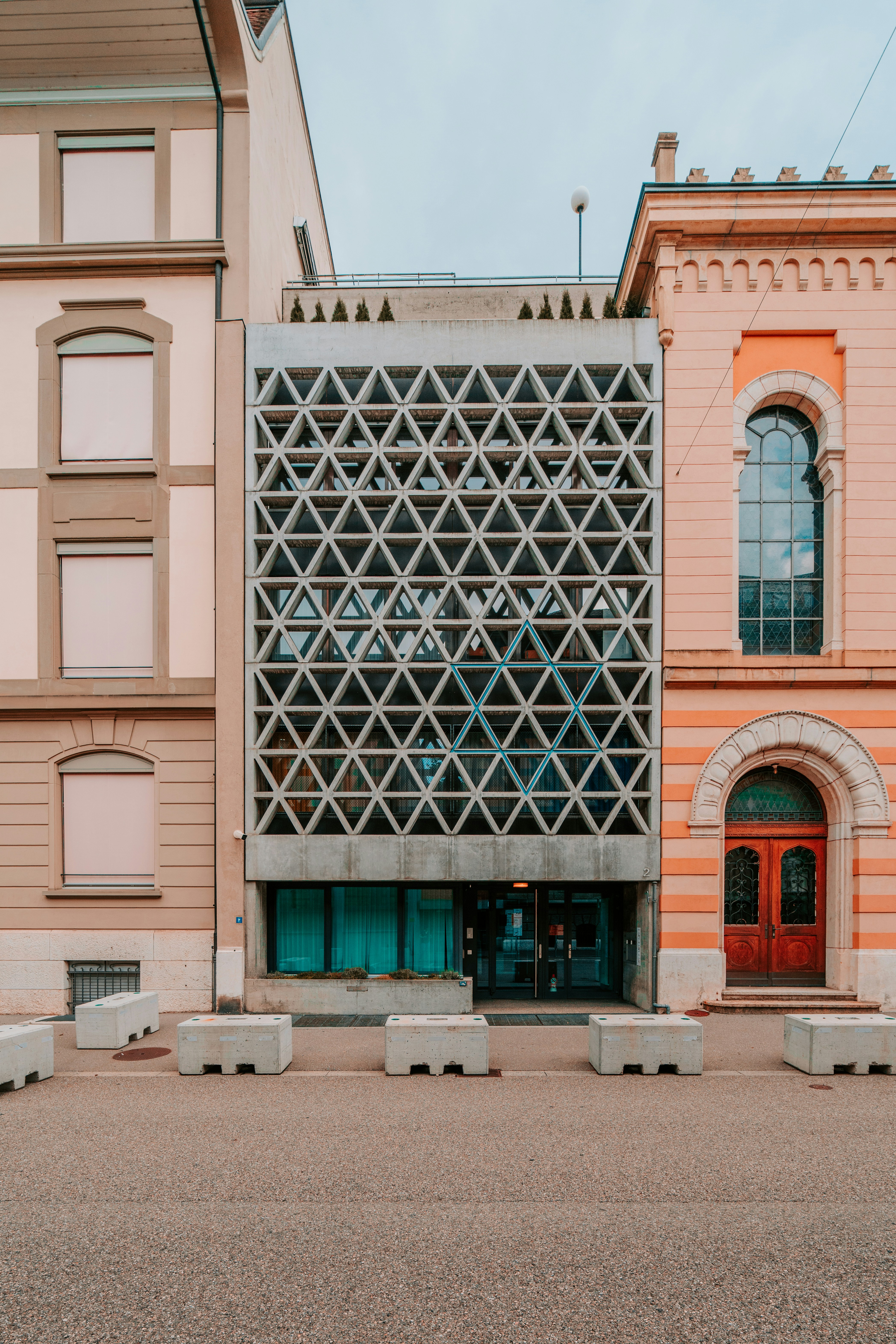 Modern concrete facade with a geometric pattern contrasts with a classic building, showcasing architectural diversity. The scene captures urban design evolution.