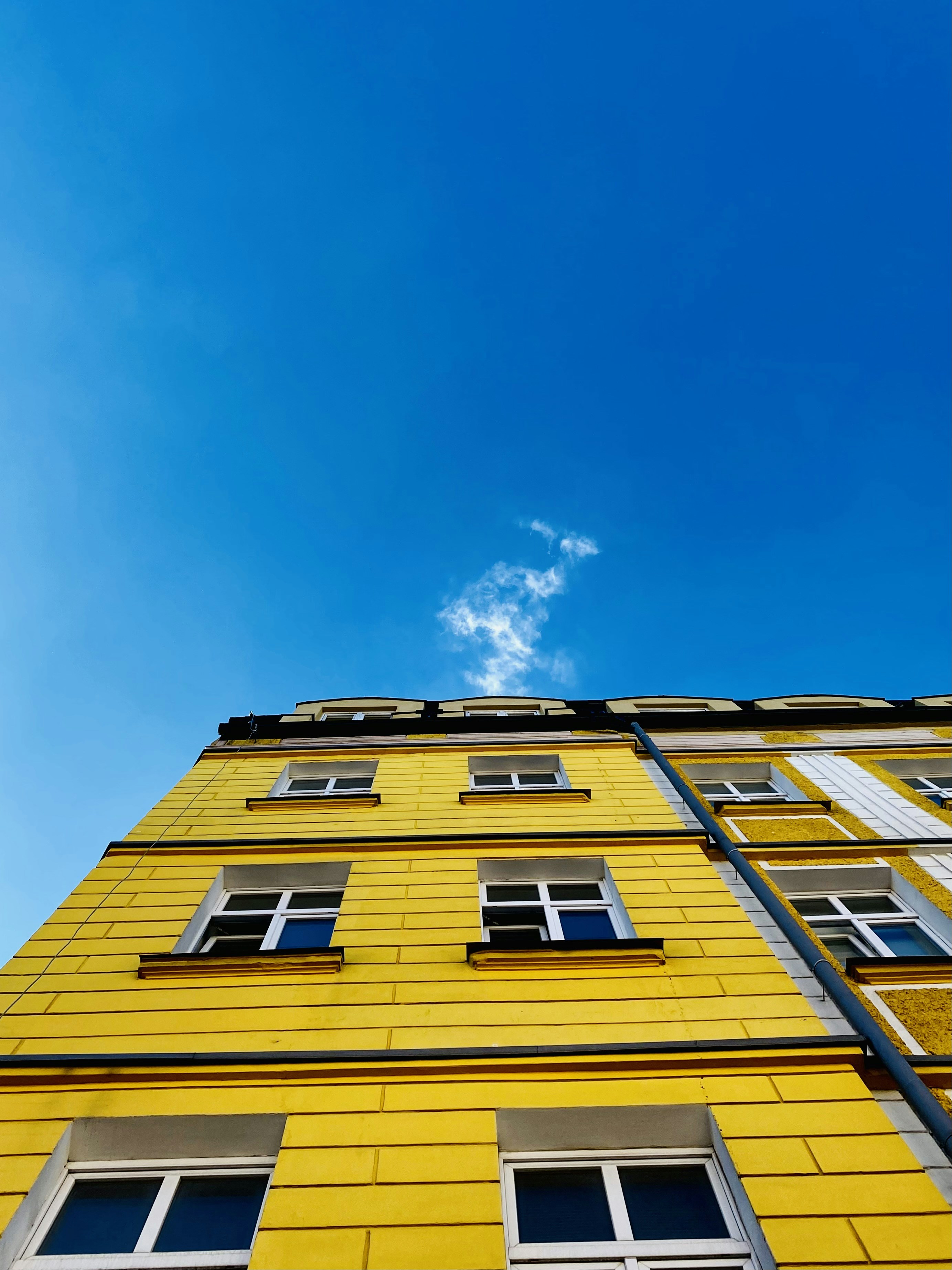Vibrant yellow building stretching skyward, contrasted by a clear blue sky with a wispy cloud. 