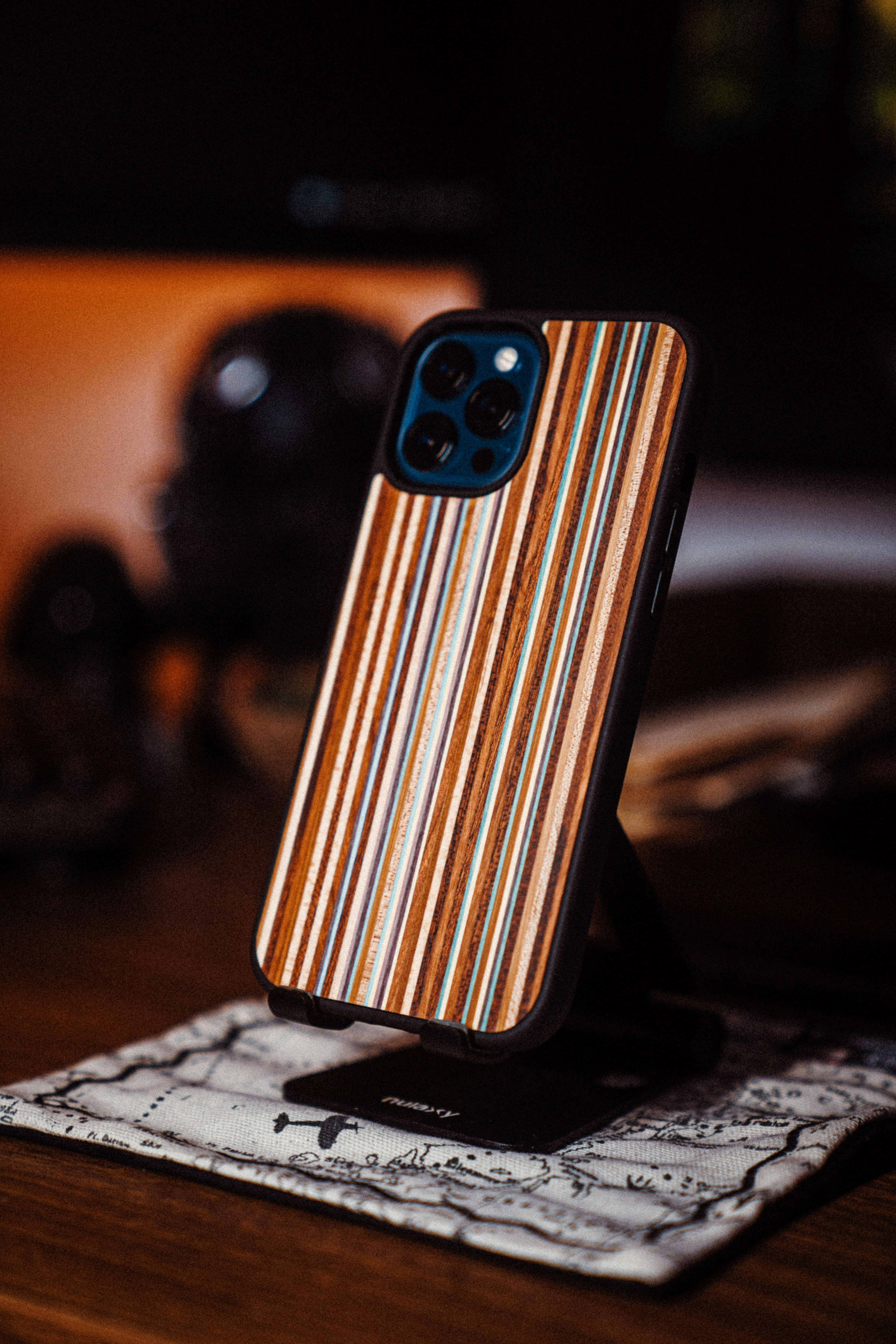 Wooden phone case with striped design resting on a patterned mat, showcasing a blend of natural aesthetics and modern technology.
