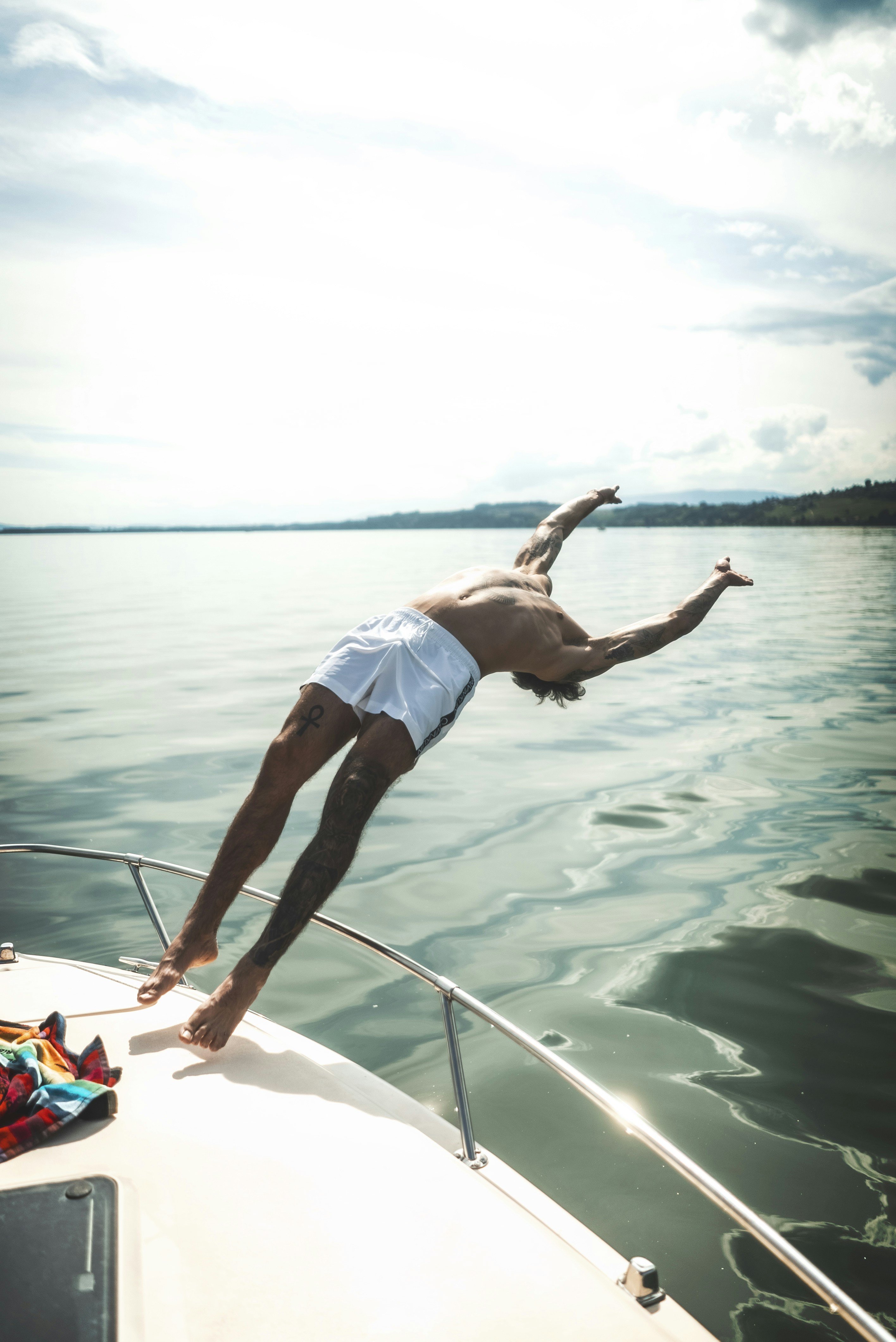 Man diving off the bow of a boat into calm waters under a cloudy sky.