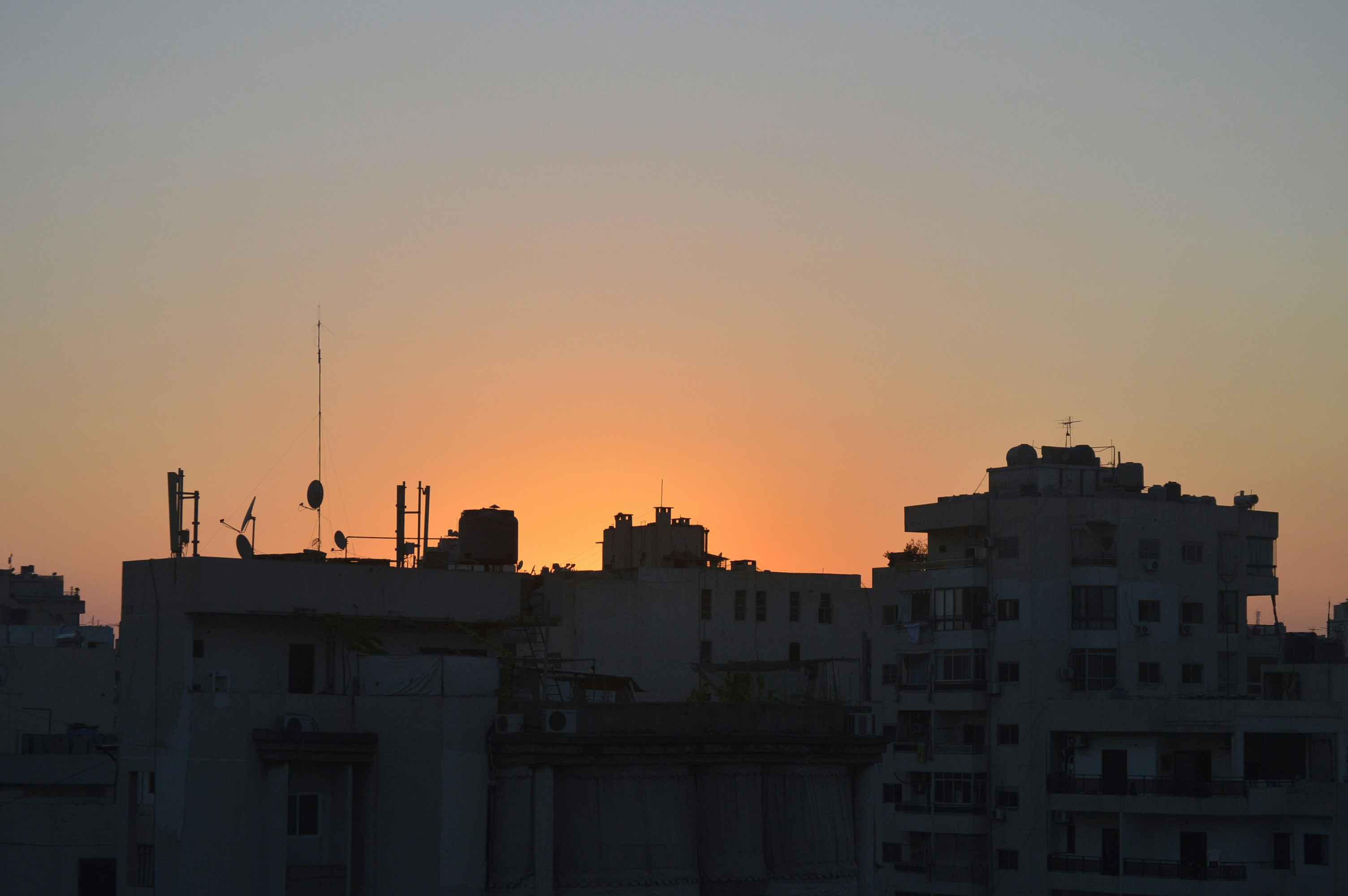 Silhouetted city skyline against a soft orange sunrise.