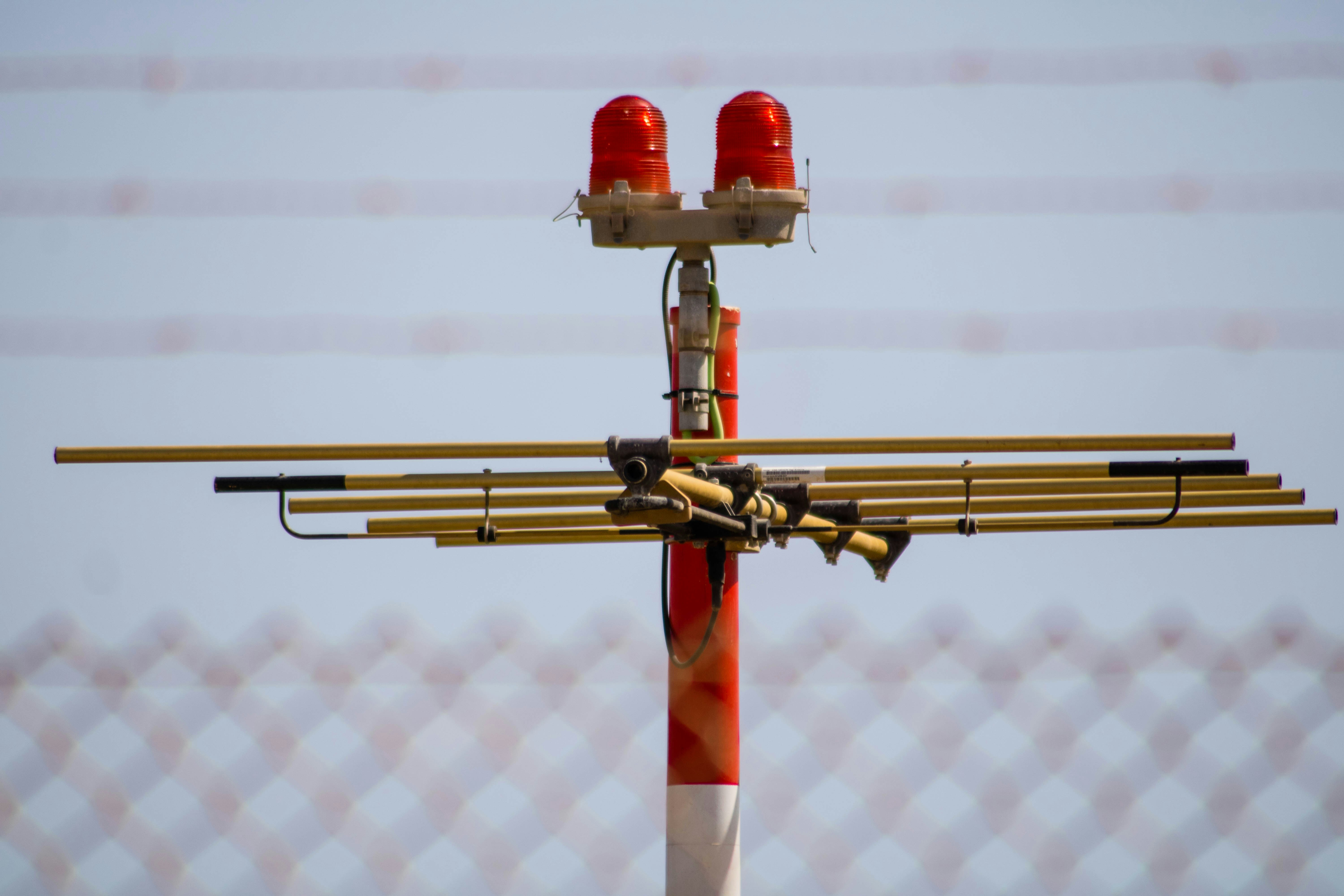 Red Safety Beacon Amid Stacked Utility Rods and Chain-Link Background