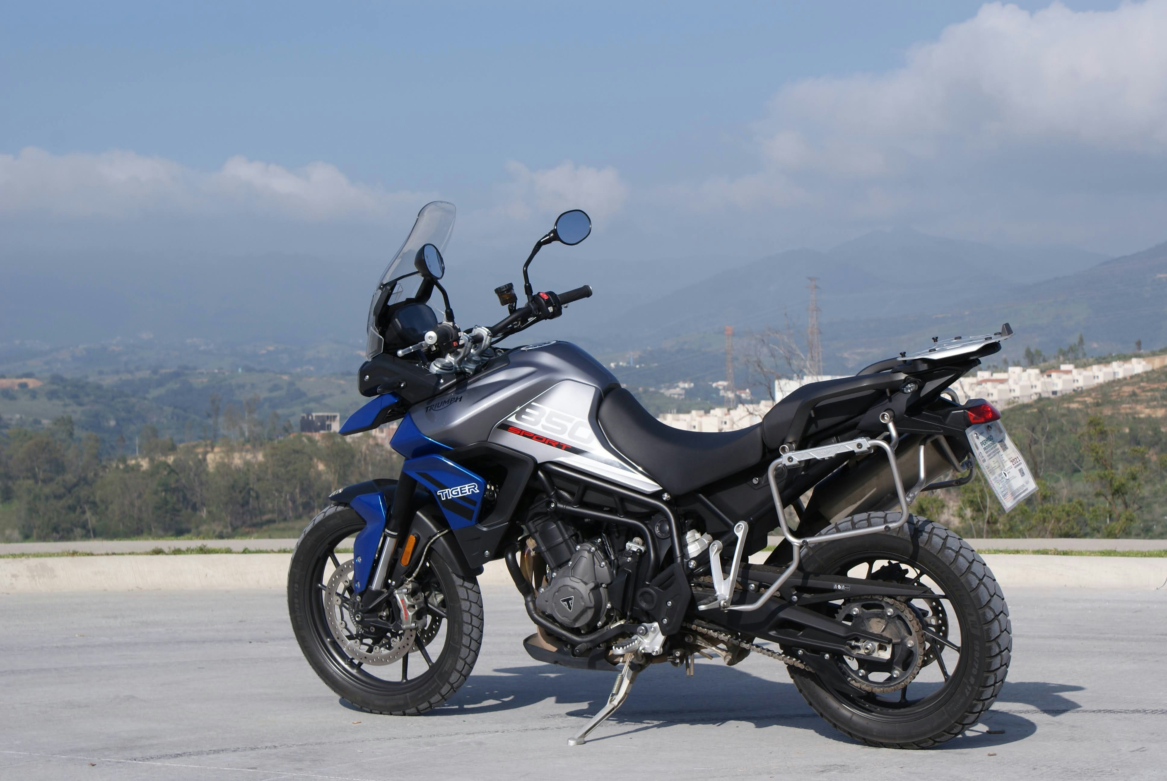Motorcycle parked on a concrete surface with mountains and blue sky in the background.