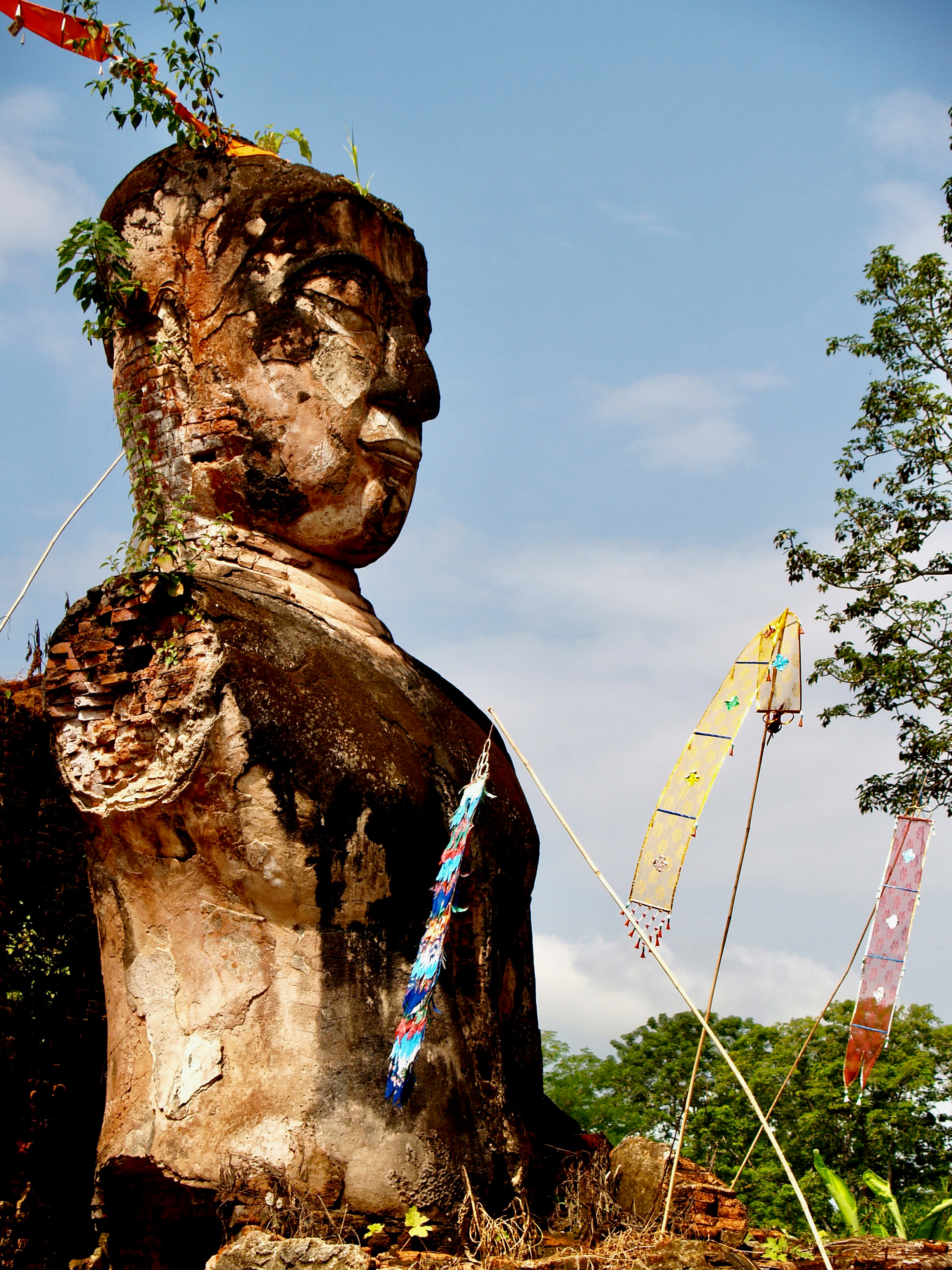 Stone Sentinel amid Ribbon Winds: A Cracked Bust in a Prayer-Flag Garden