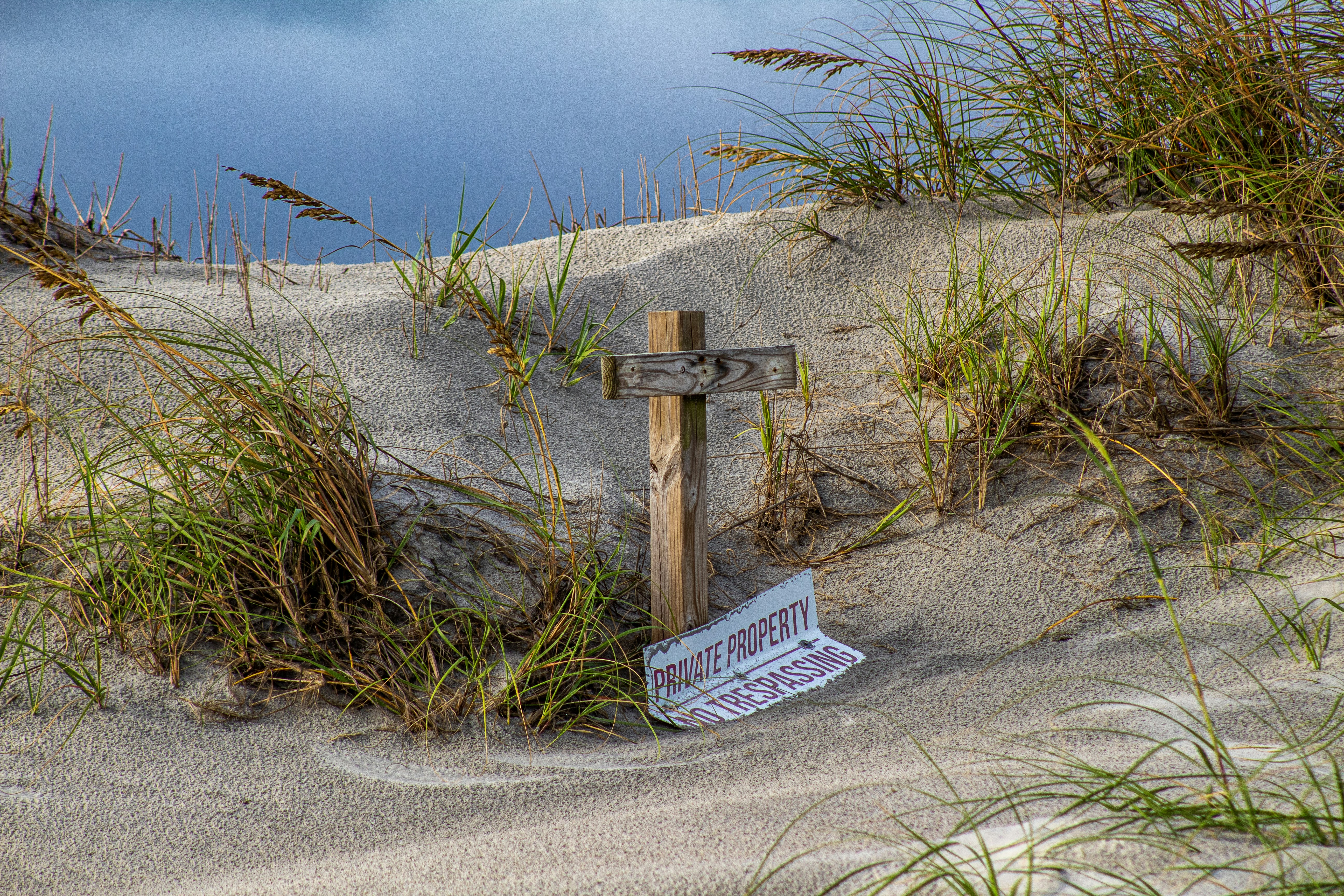Weathered wooden sign marking private property amidst soft sand dunes and coastal grasses.