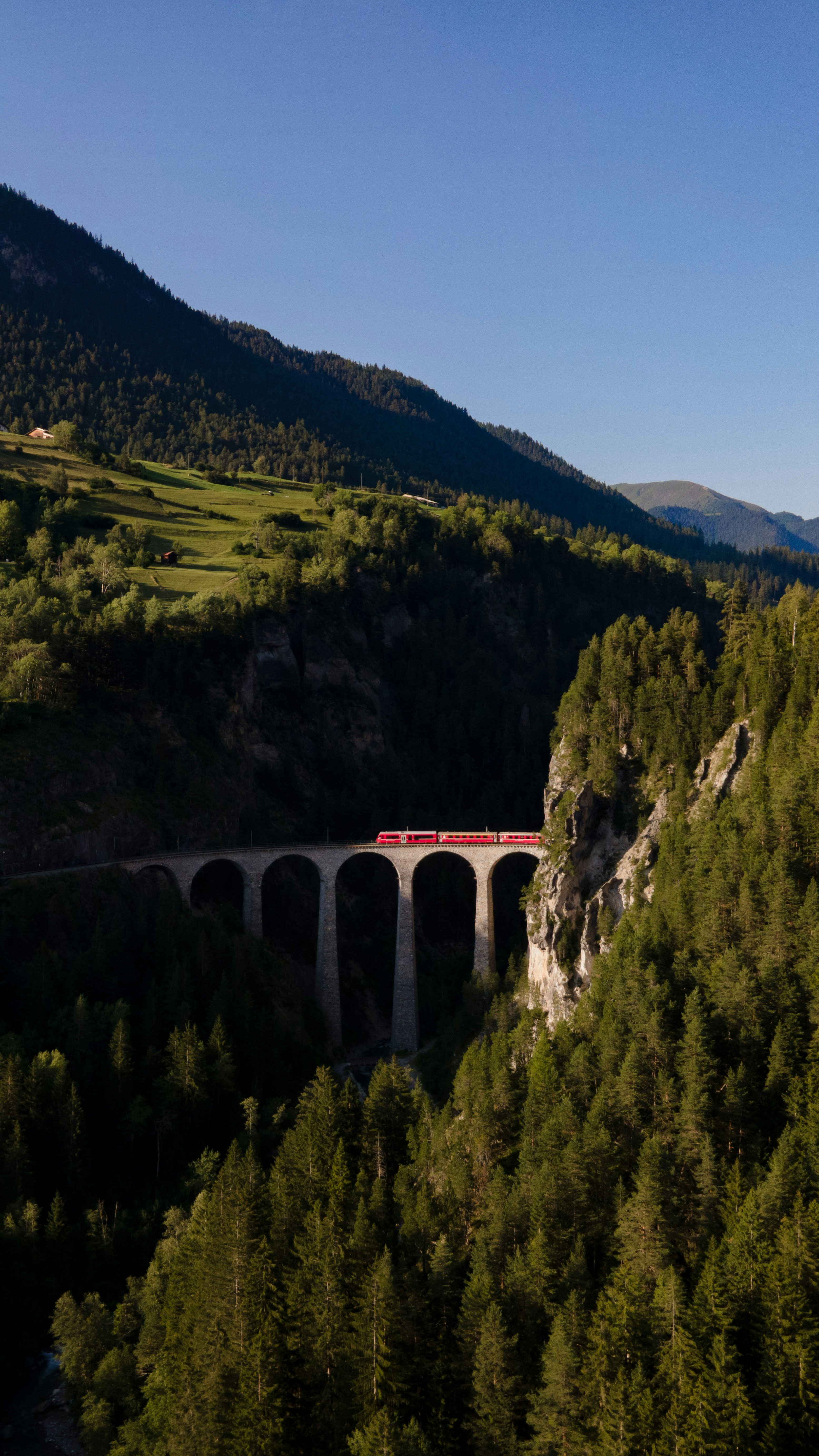 Crimson Locomotive on the Alpine Viaduct Amid Verdant Valleys