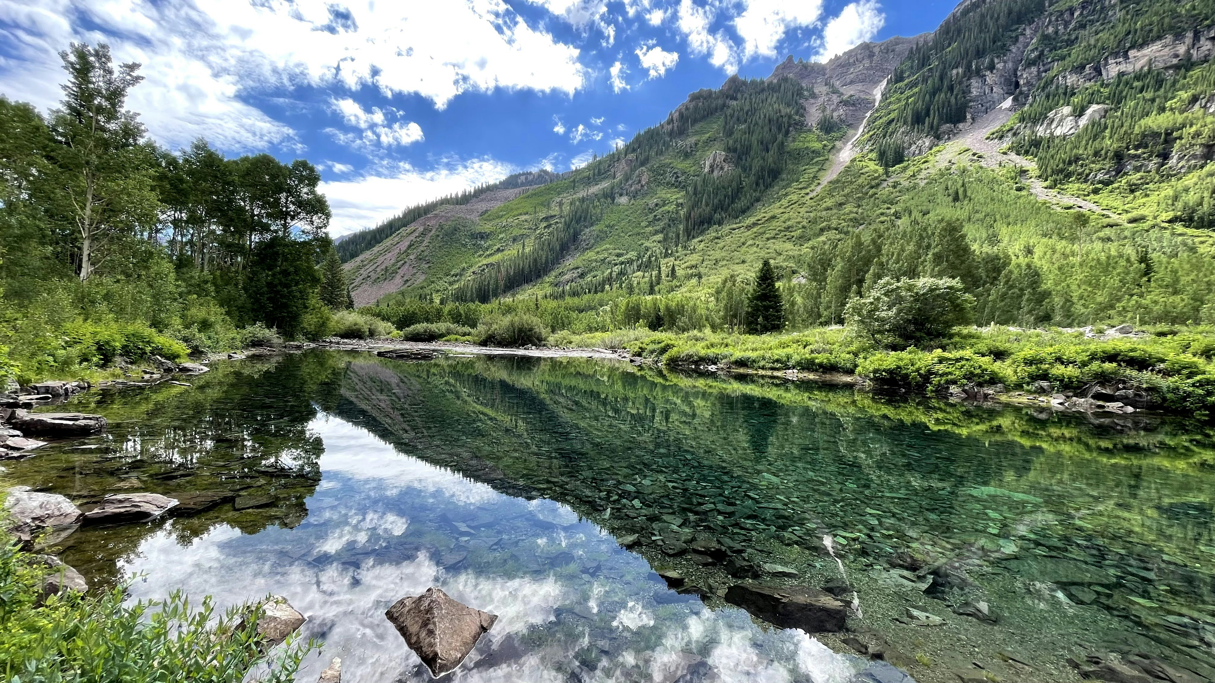 green trees and mountain beside river under blue sky during daytime