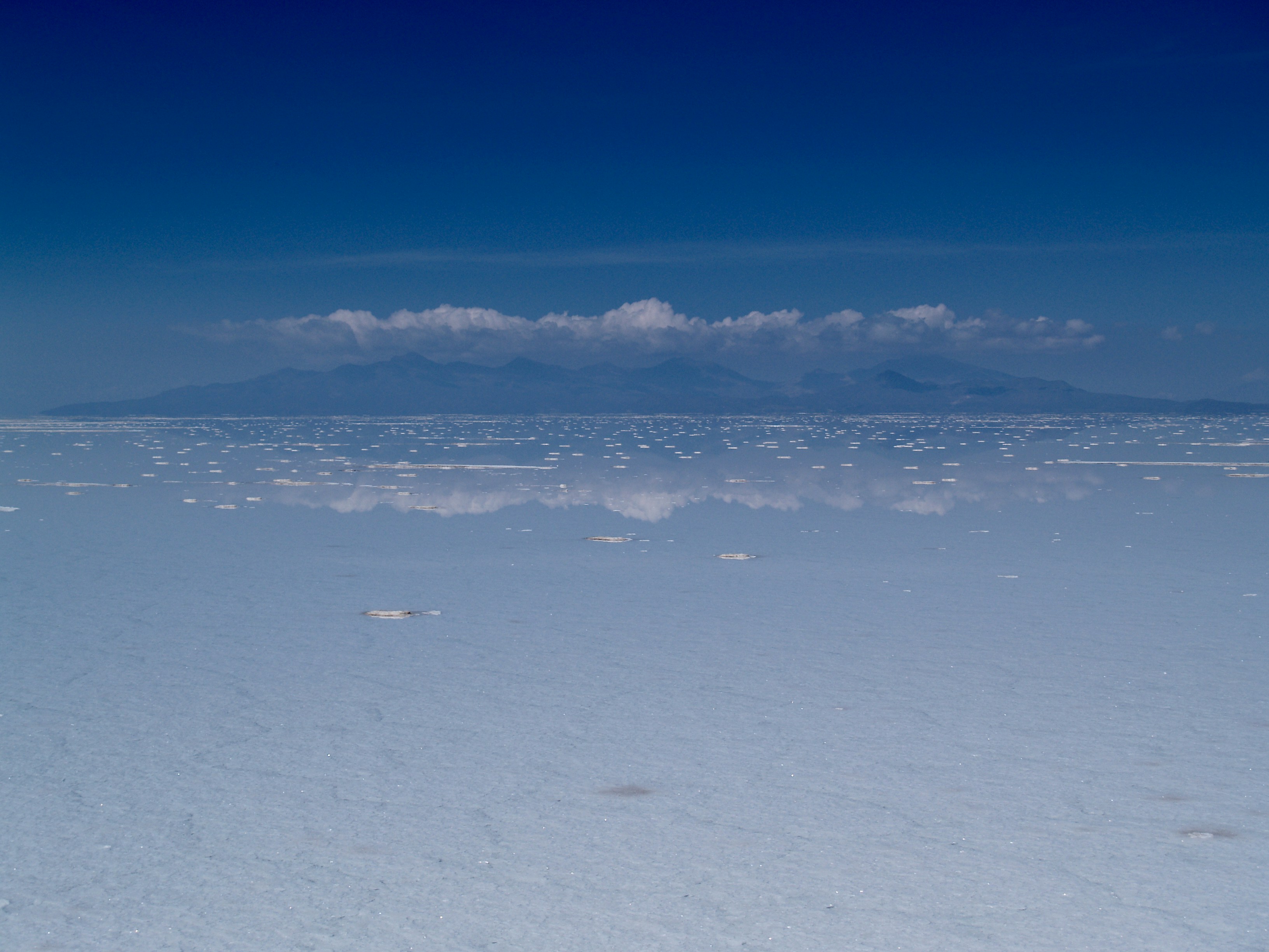 Vast salt flat reflecting a tranquil sky and distant mountains, creating a seamless horizon. The scene embodies serenity and the beauty of nature's simplicity.