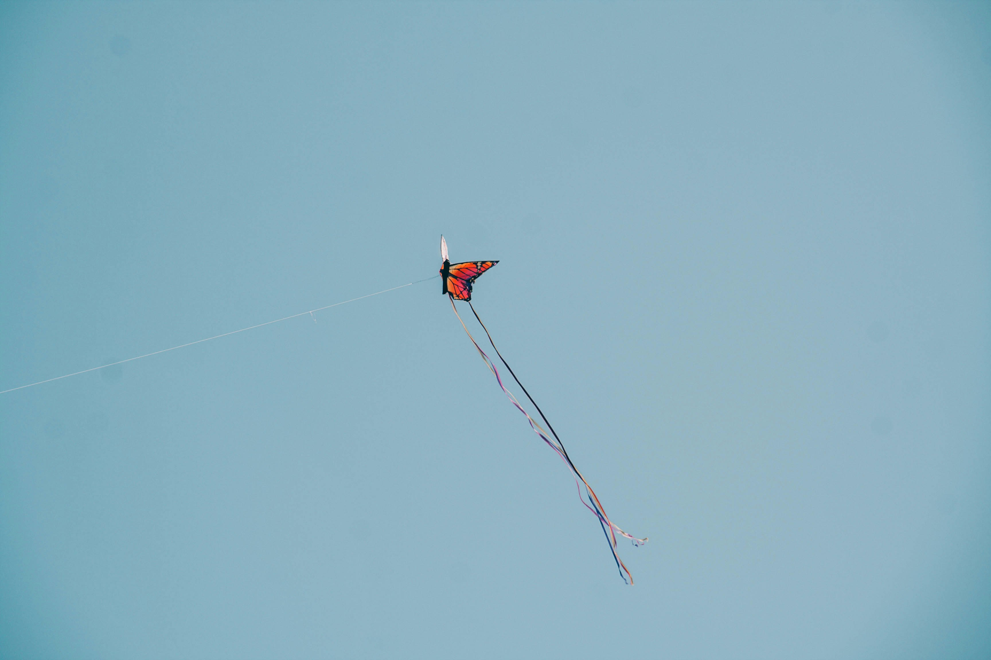 Colorful butterfly-shaped kite soaring against a clear blue sky, trailing vibrant ribbons below.