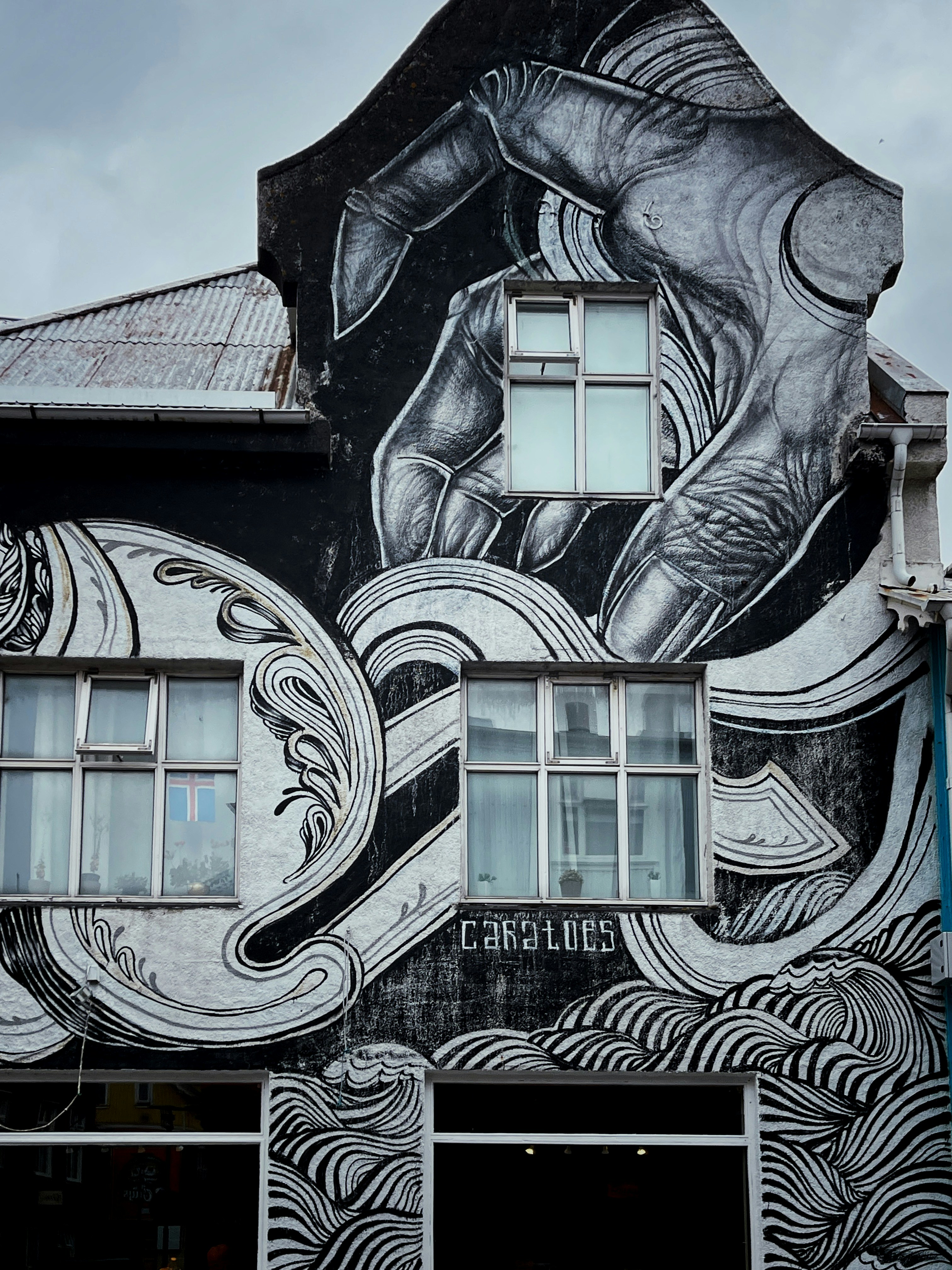 Urban mural of a giant curled hand over a storefront facade