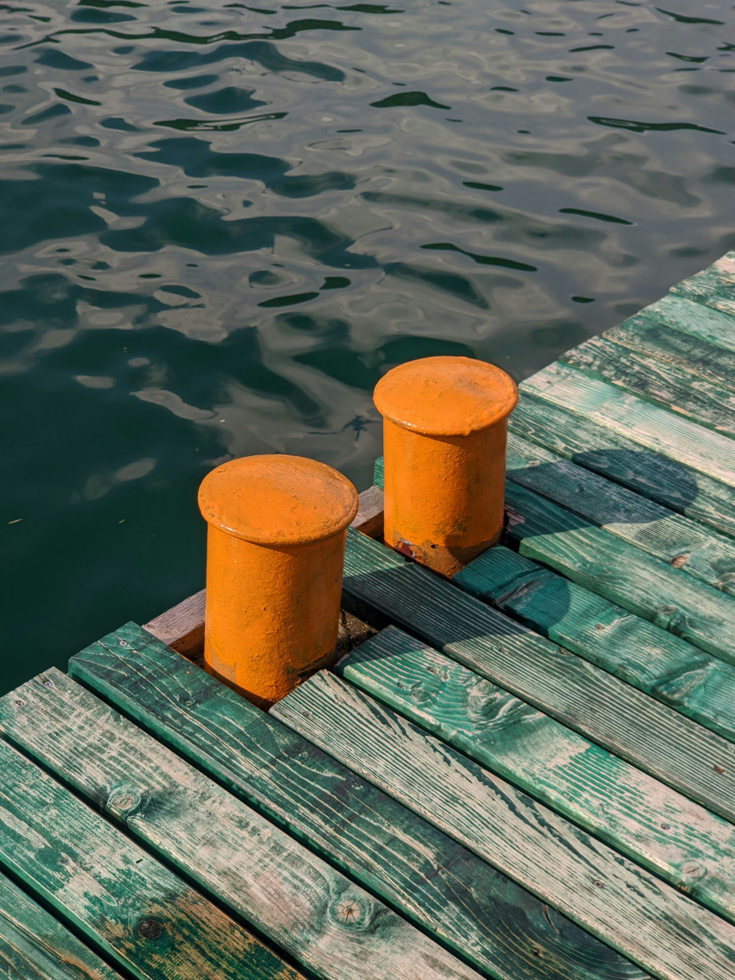 Rusty orange bollards anchor a weathered teal dock beside calm water