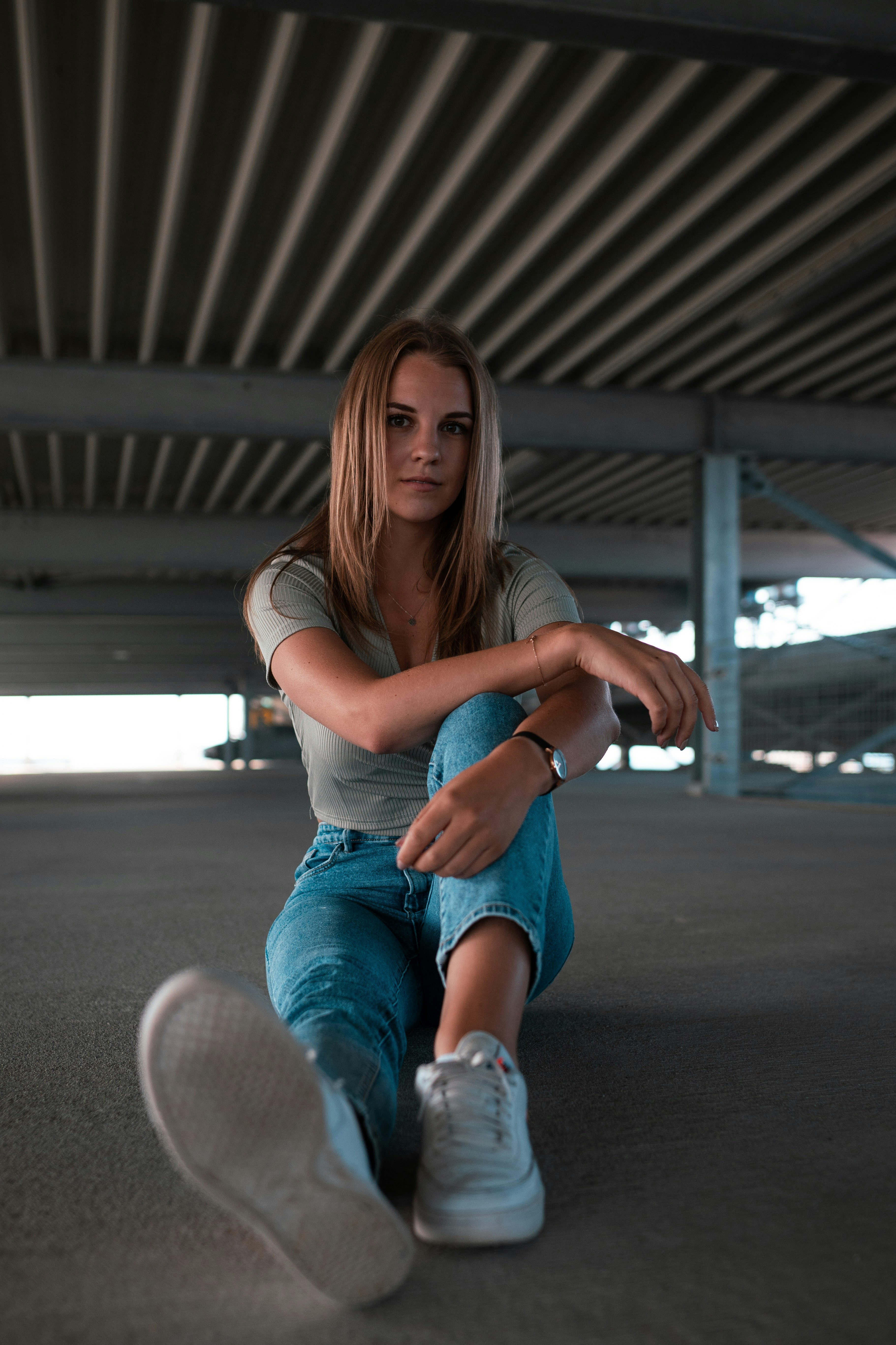 Young woman seated on the ground in a parking garage, exuding calmness amidst industrial surroundings.