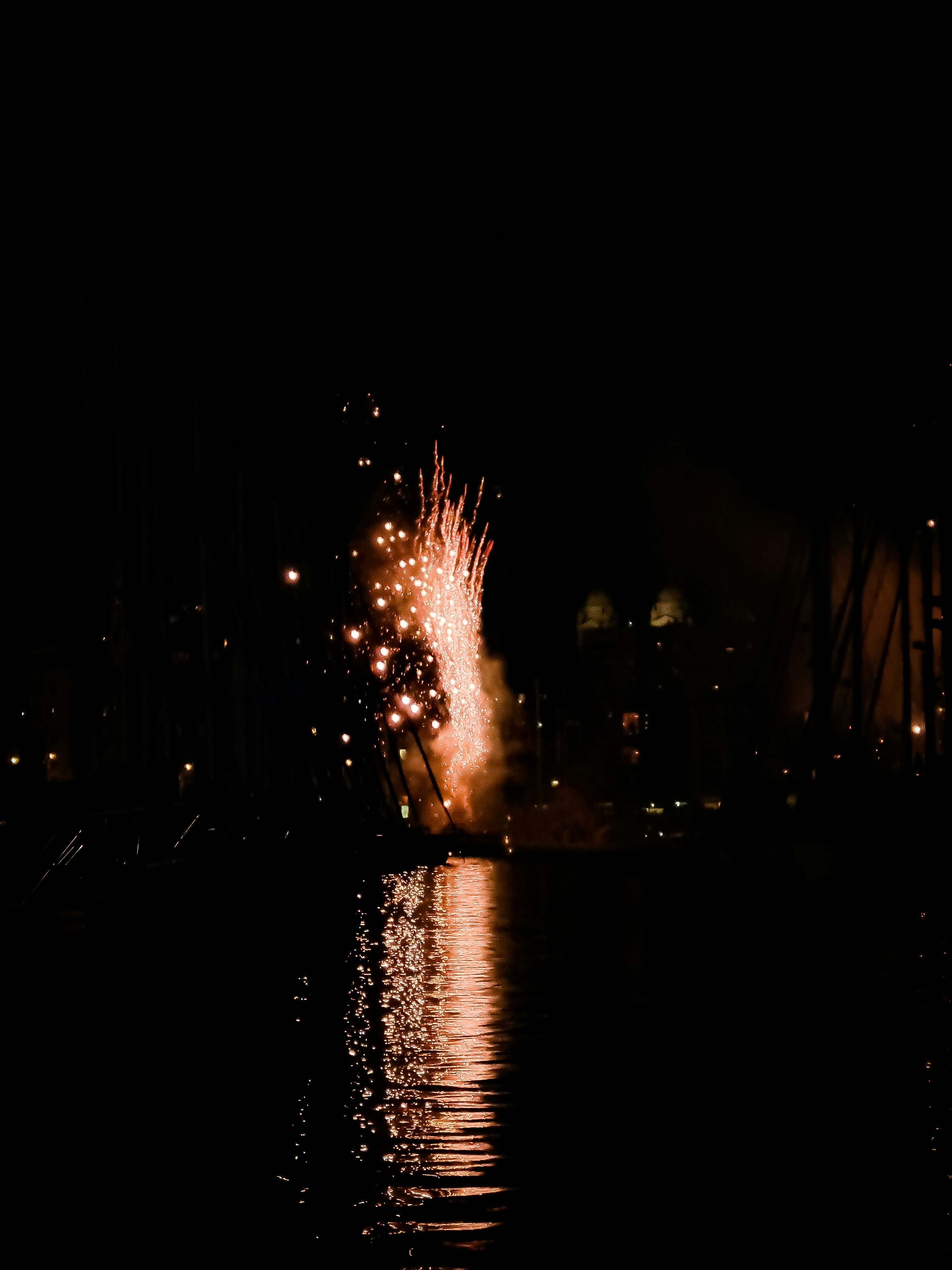 Fireworks erupting over water, creating a dazzling display of light and reflection against a dark backdrop.