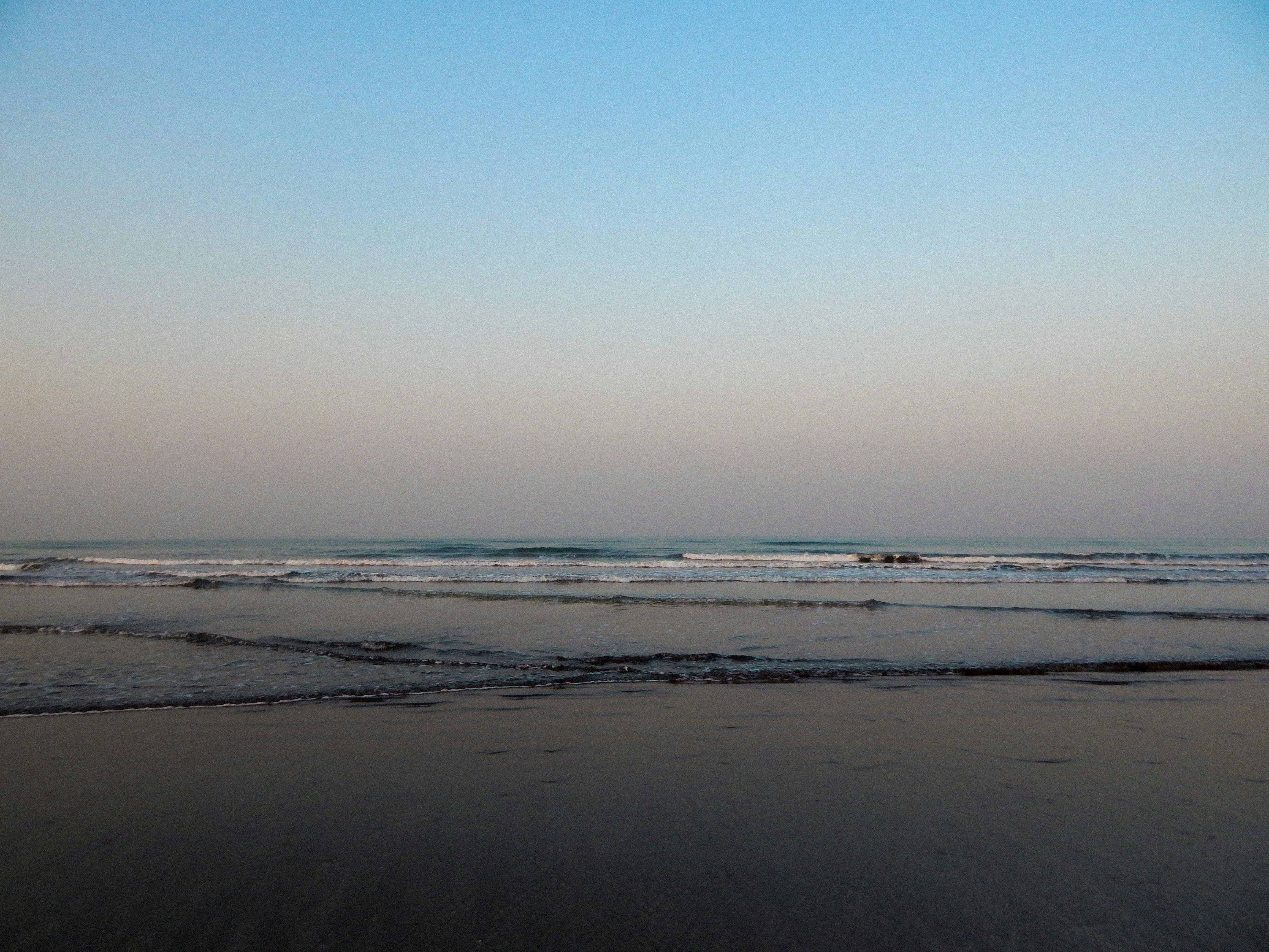 Gentle waves lapping against a tranquil shoreline under a soft blue sky. The scene evokes a sense of calm and reflection.