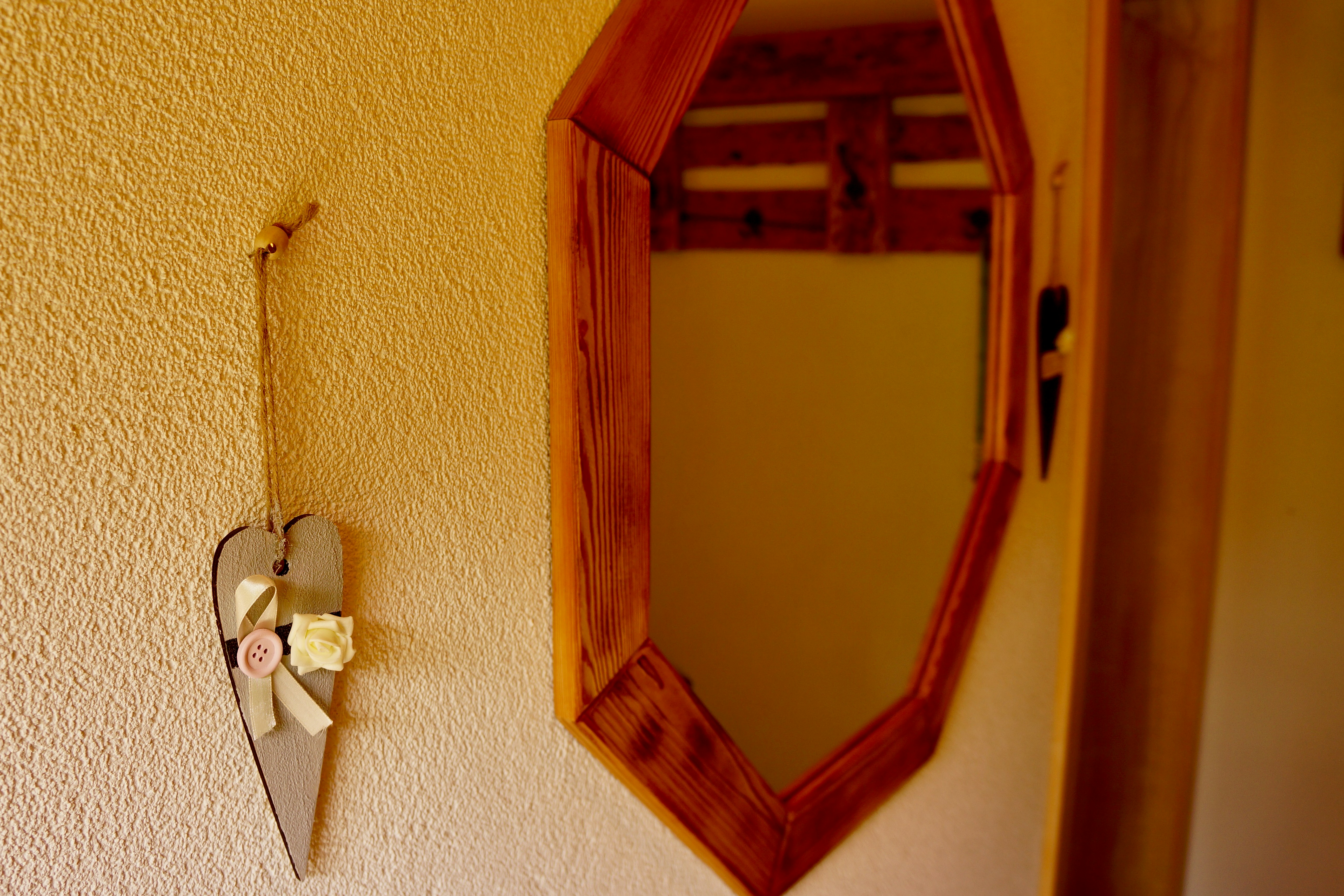 Decorative heart-shaped ornament hanging on a textured wall beside an octagonal wooden mirror.