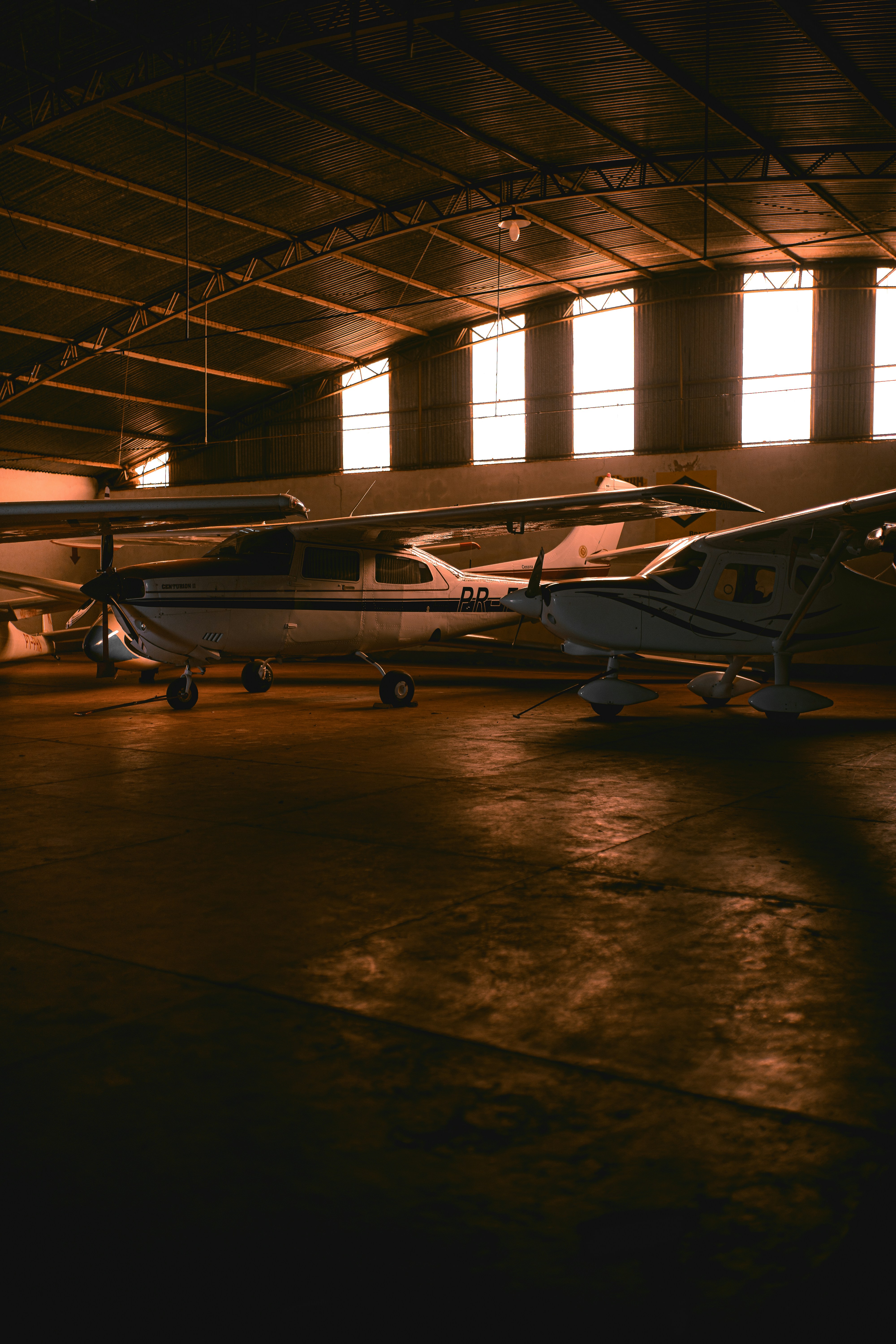 Two small aircraft resting in a dimly lit hangar, illuminated by soft light filtering through the windows.