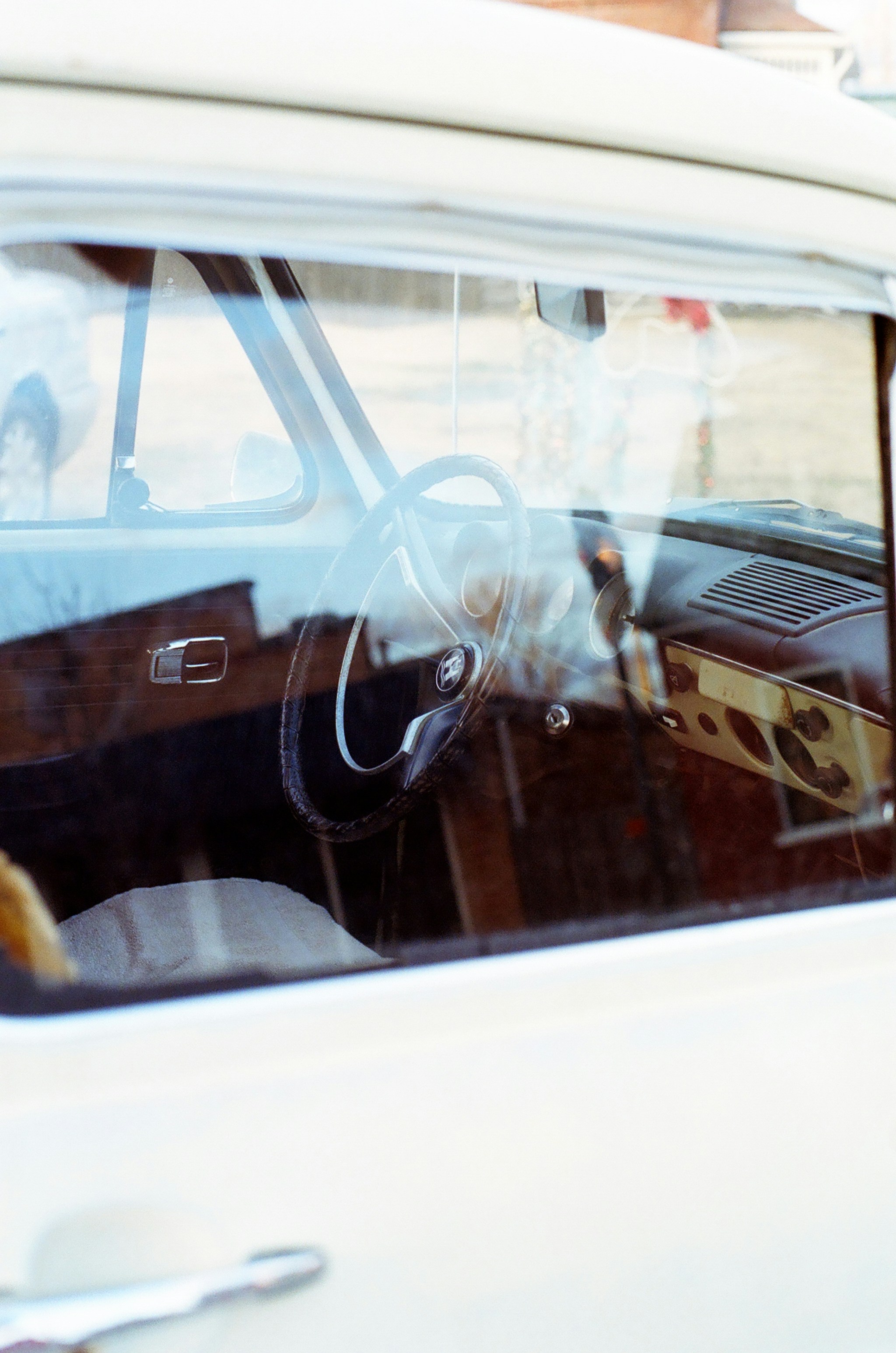 Interior view of a vintage car showcasing the steering wheel and dashboard through the glass window. The scene evokes a sense of nostalgia.