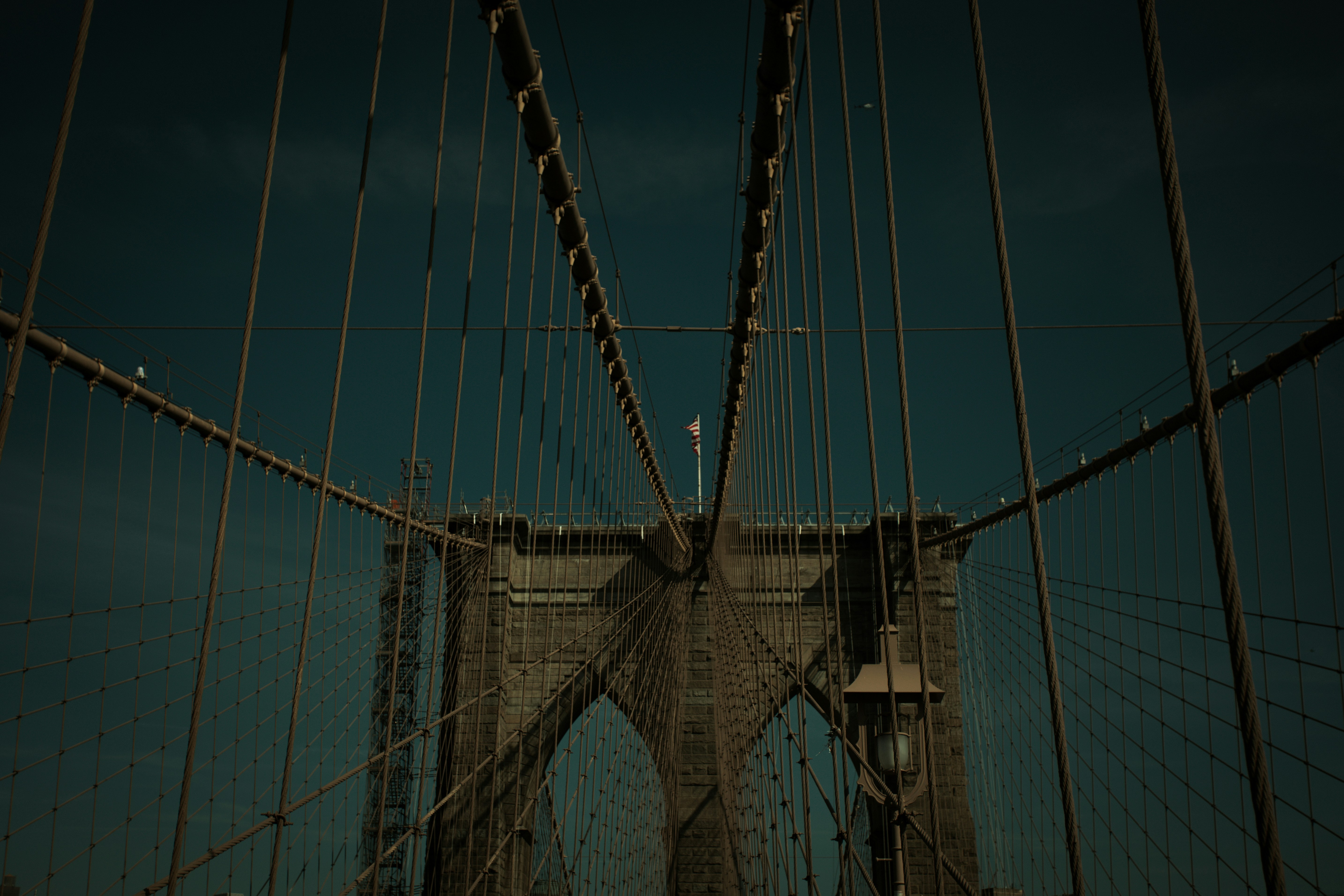 The intricate network of cables and stonework of the Brooklyn Bridge creates a striking perspective against a moody sky.
