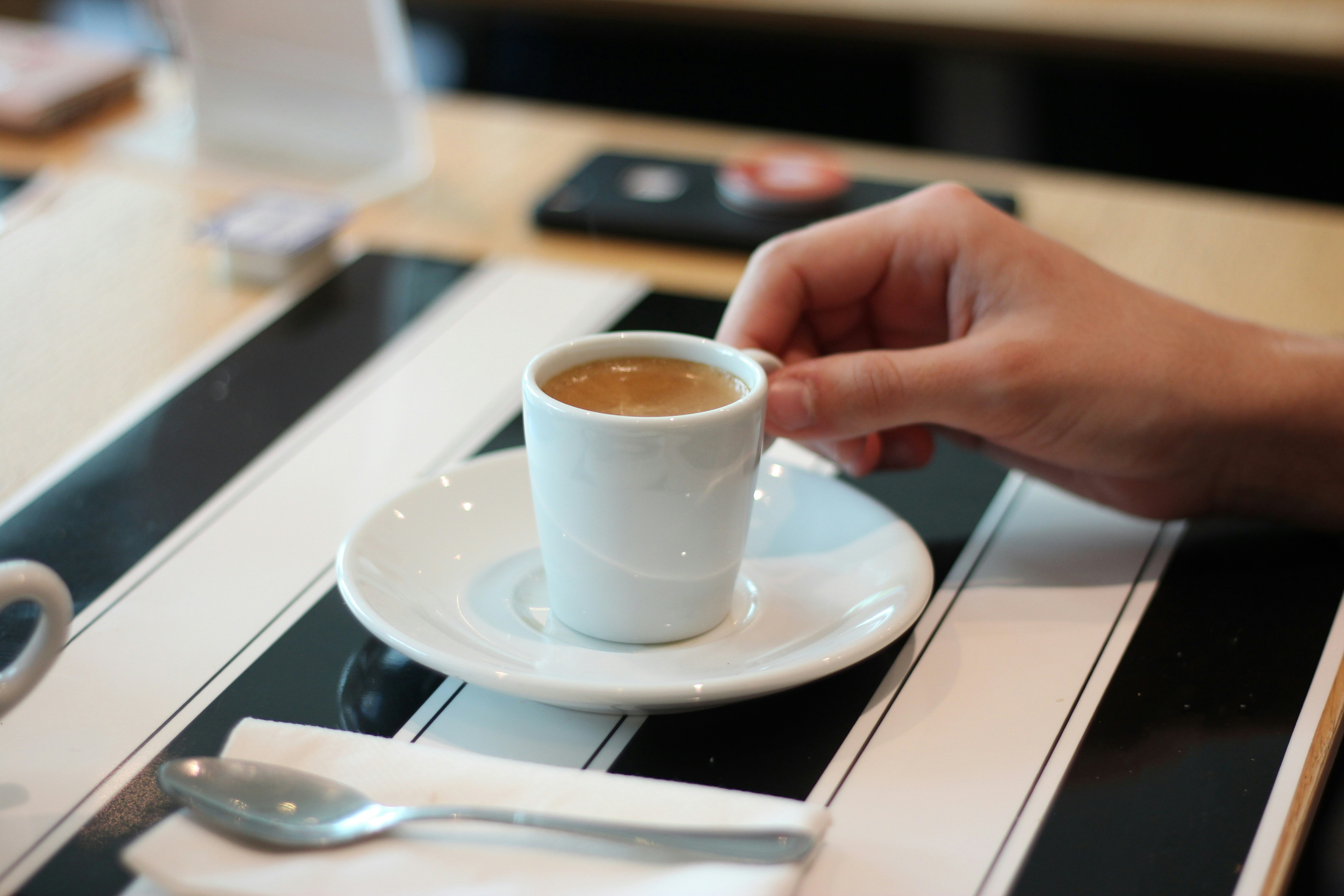 Espresso on a Monochrome Canvas: A Hand Reaches for Warmth Across Striped Table