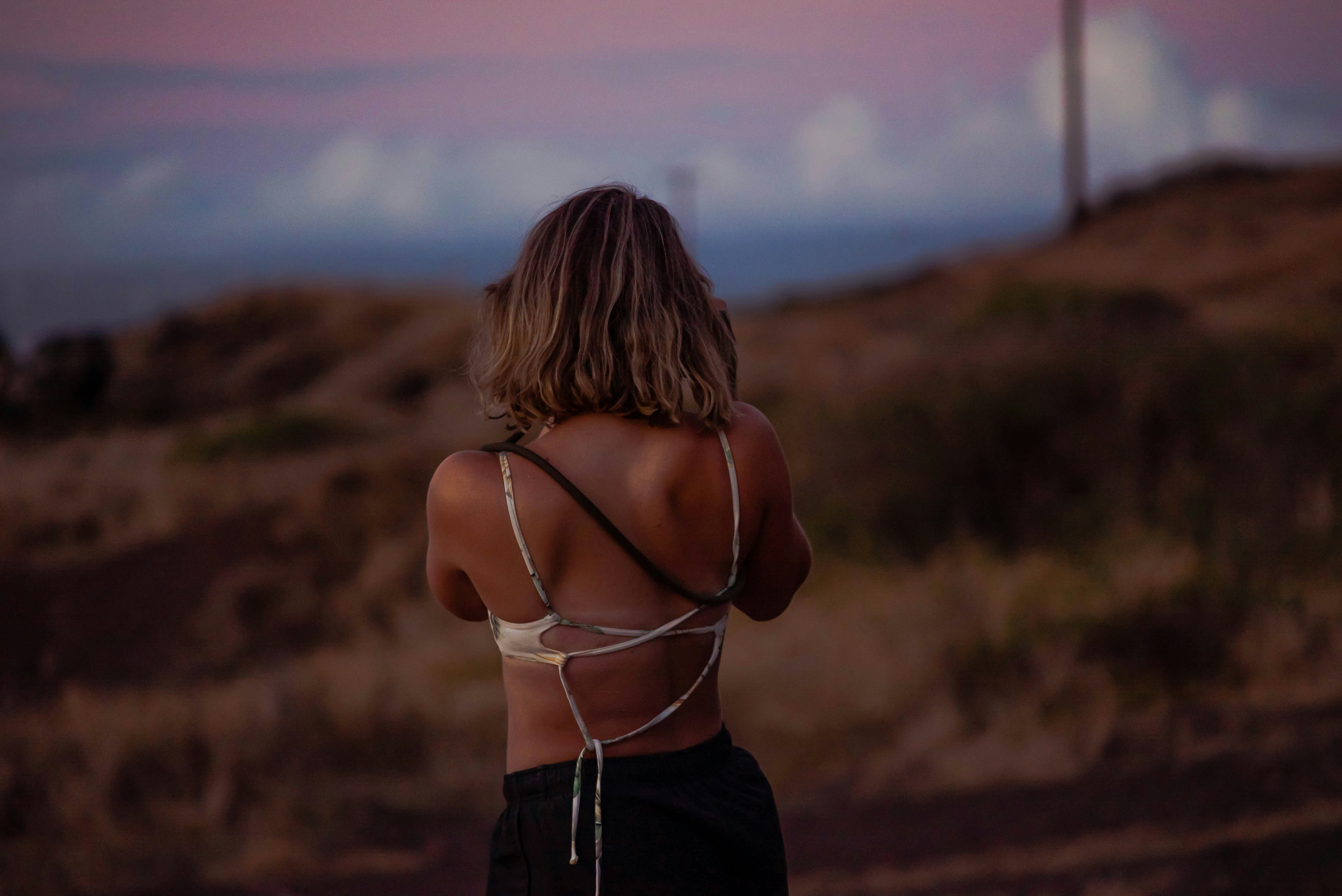 Woman's back in a bathing suit as she takes a picture of the sunset while hiking on Oahu
