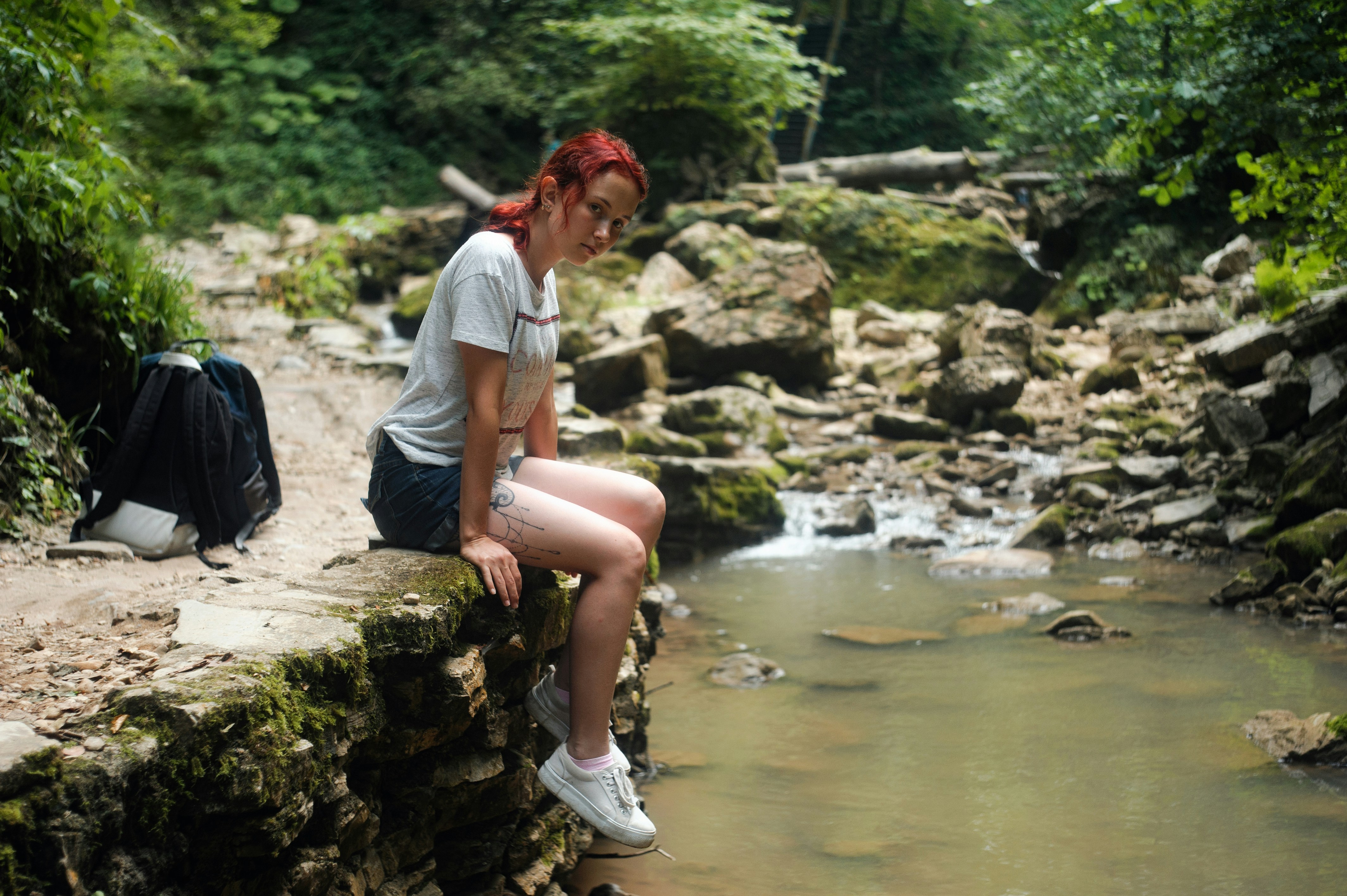Woman sitting on a rock beside a gentle river, surrounded by lush greenery and sunlight.