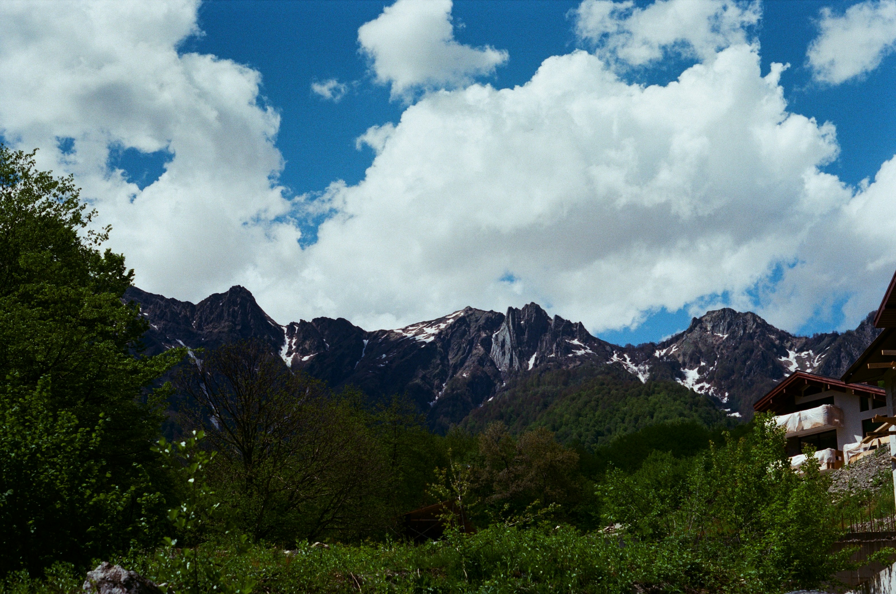 Majestic mountain range under a dynamic sky, showcasing lush greenery in the foreground and snow-capped summits in the background.