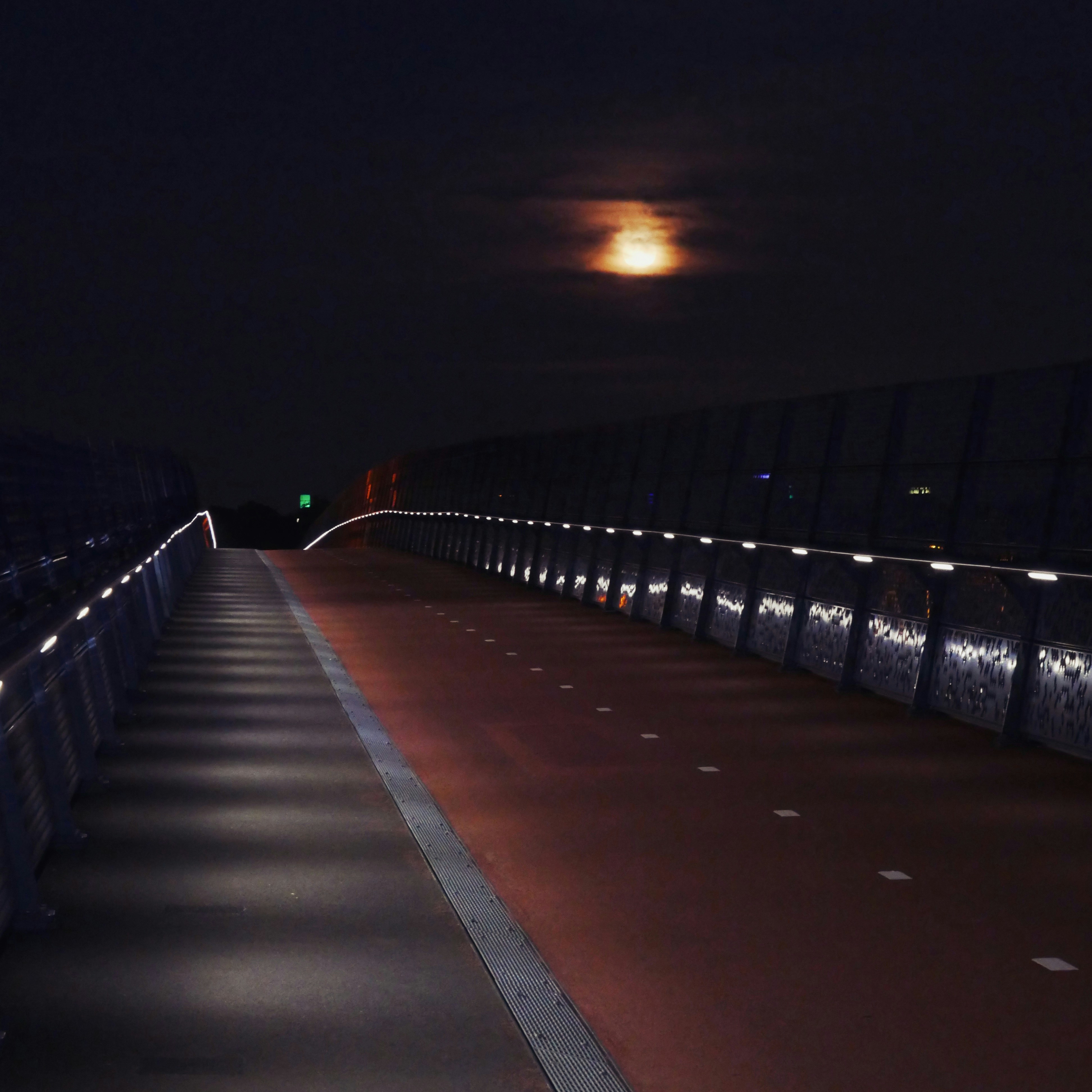 Illuminated pathway under a cloudy night sky, with a glowing moon peeking through. The scene captures the tranquility of a nighttime stroll.