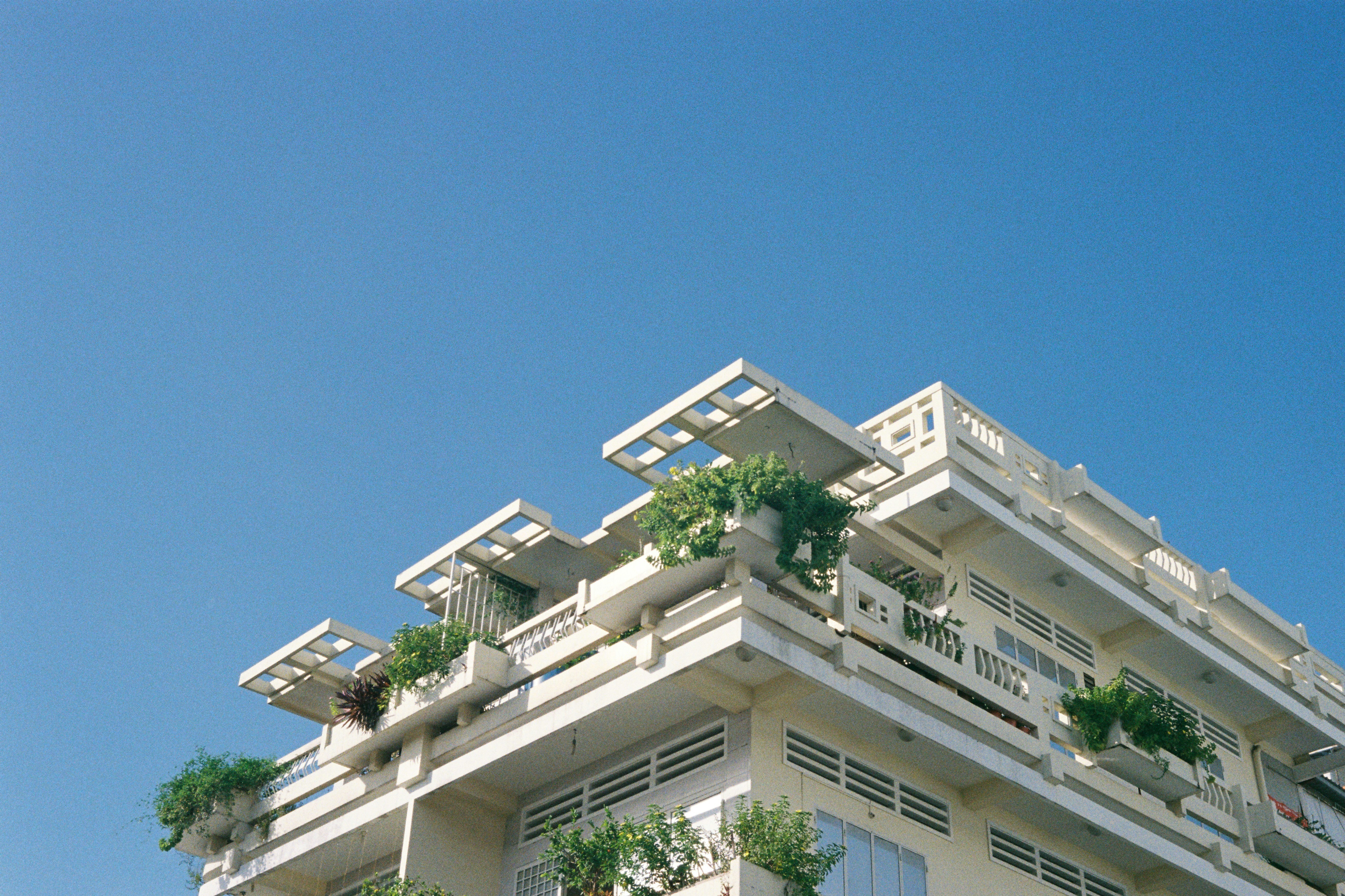 Modern apartment building adorned with lush greenery and unique architectural features against a clear blue sky.