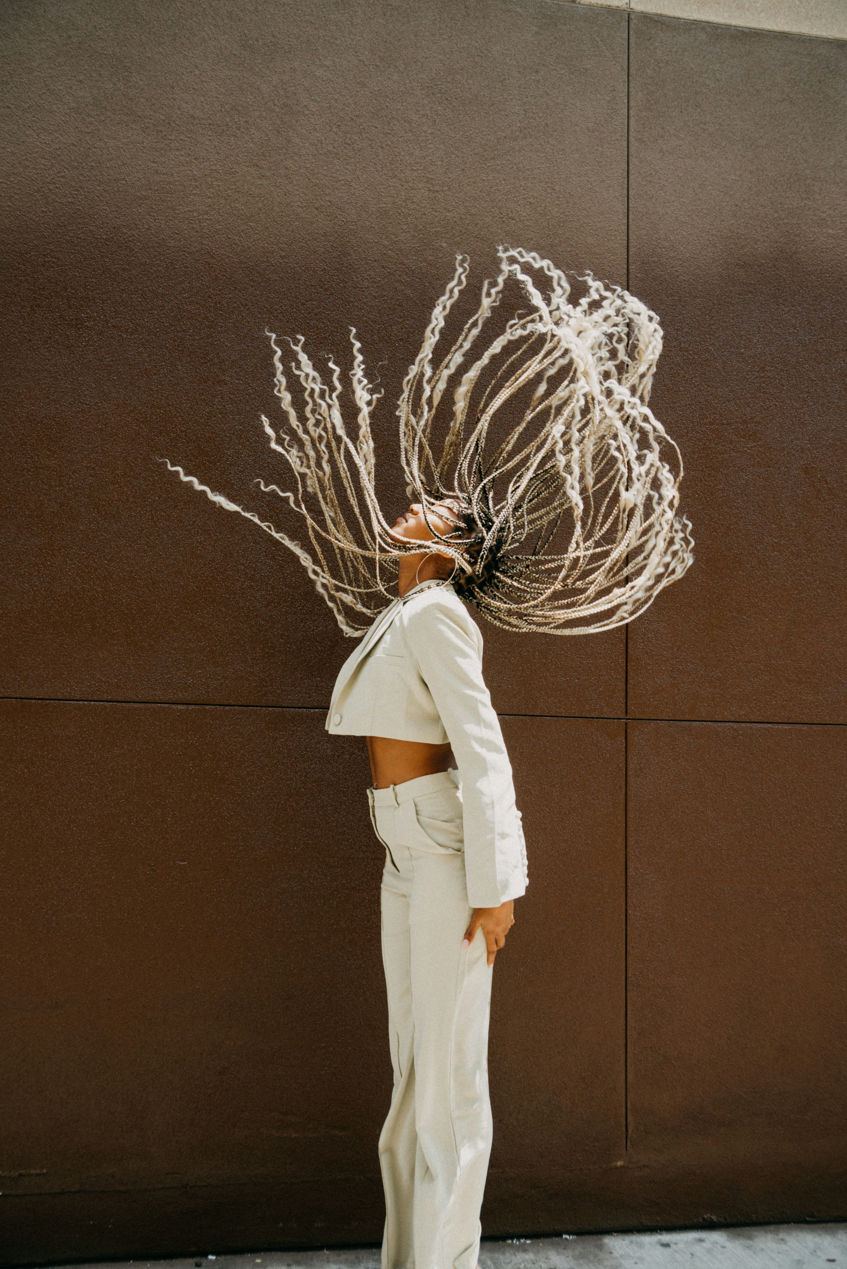 Model in a white outfit showcasing dynamic hair movement against a textured brown background.