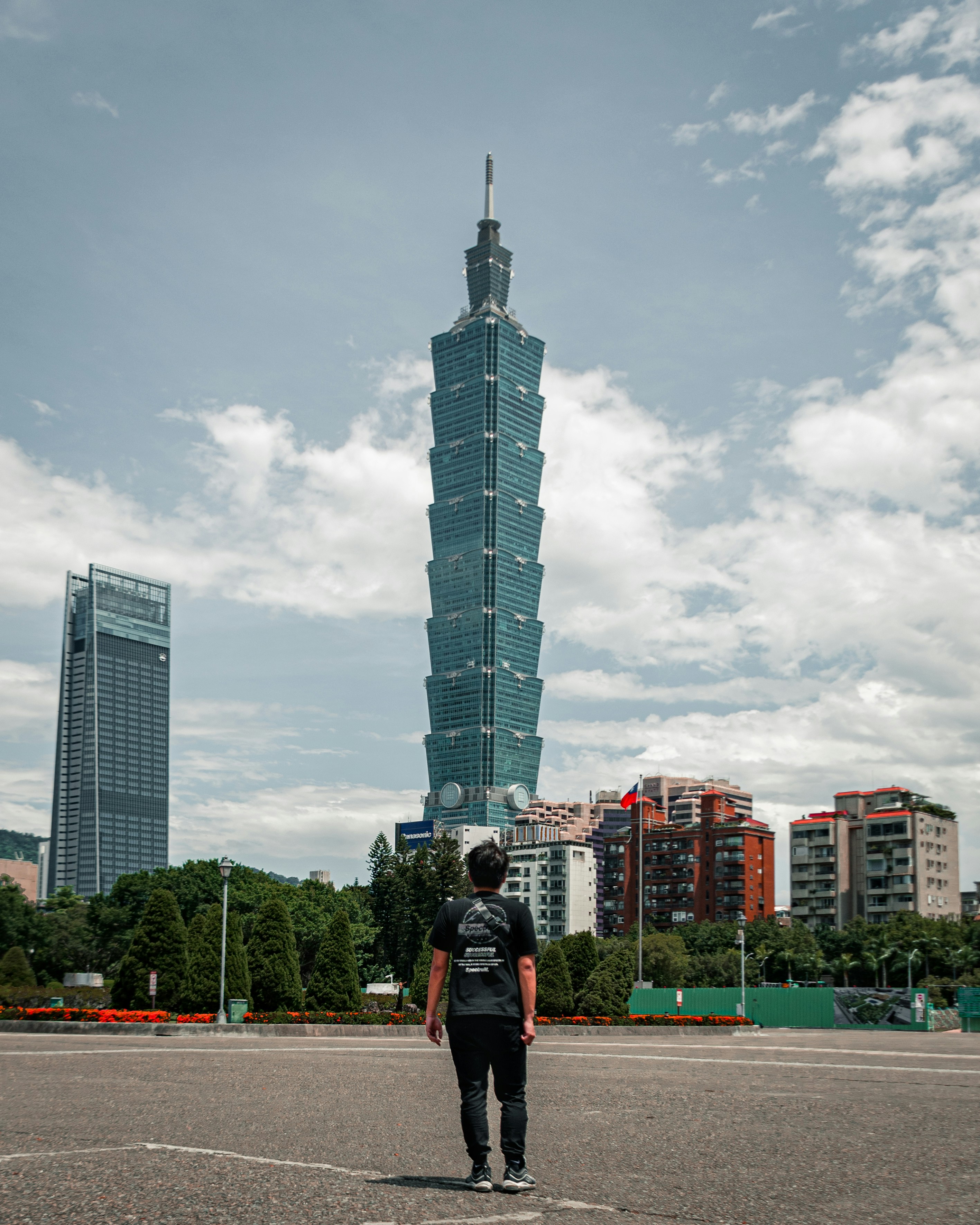 man in black jacket and black pants standing on gray concrete road near city buildings during
