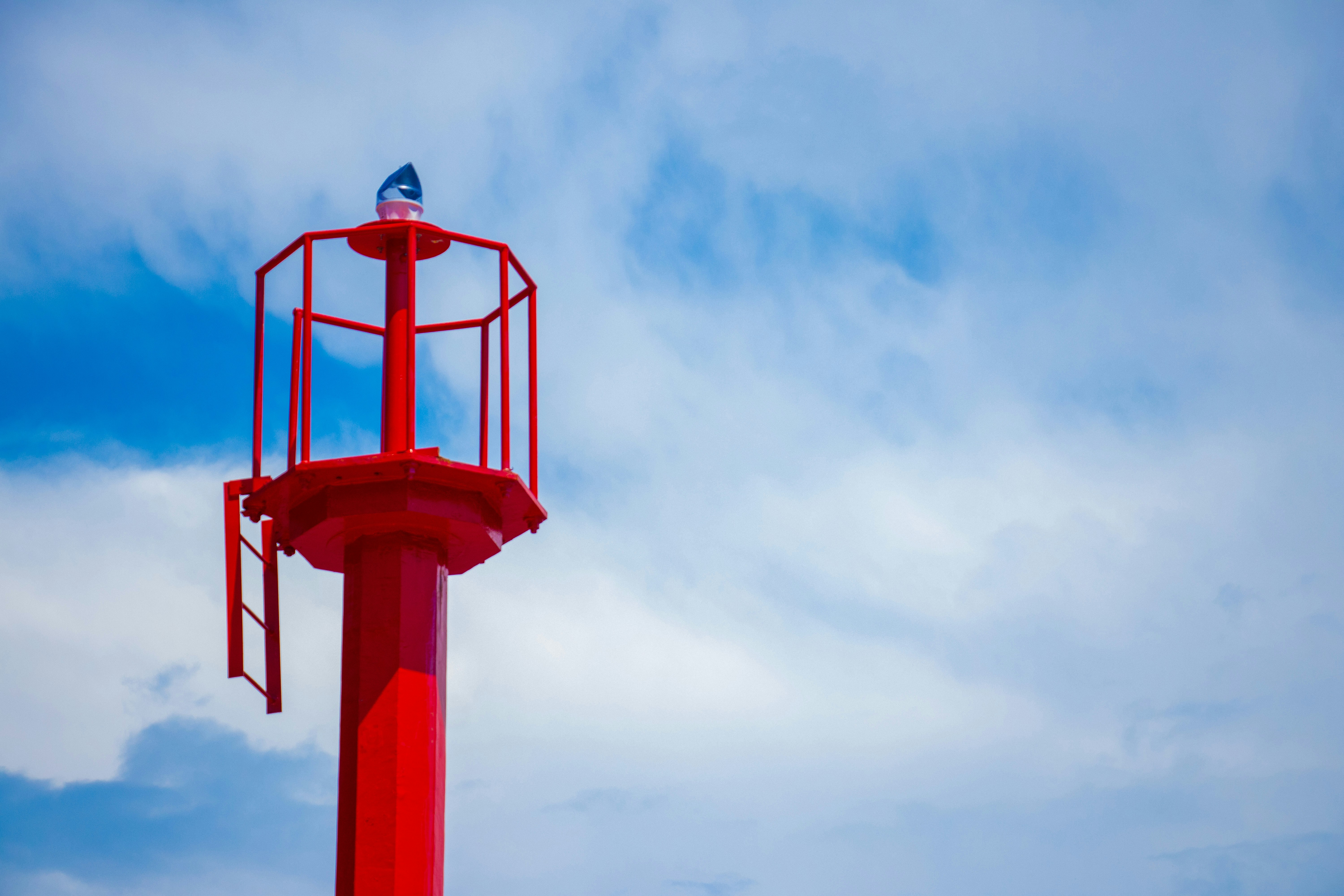 Red lighthouse tower stands tall against a backdrop of blue skies and wispy clouds.